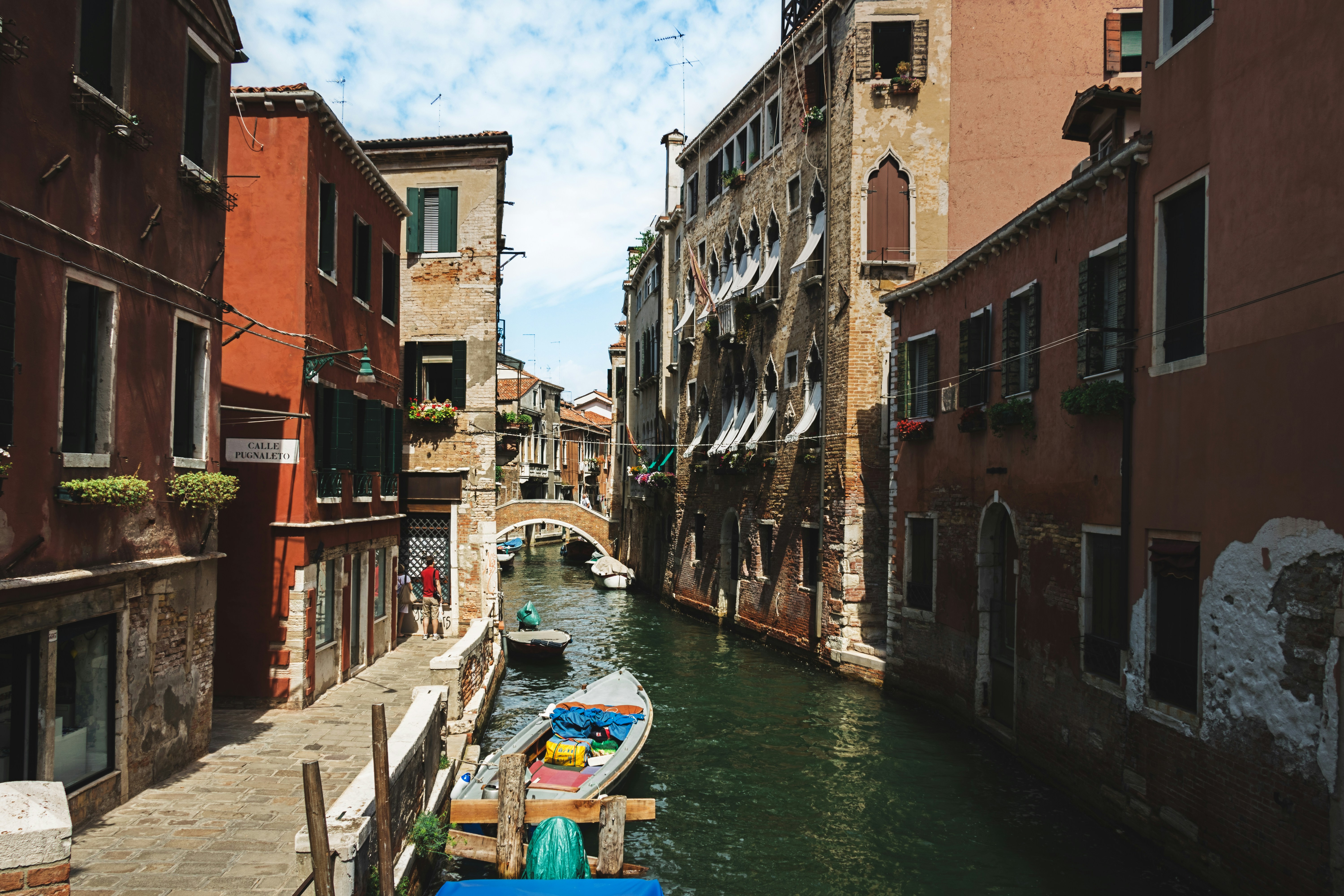 Motorboat docked on a narrow canal between sunlit Venetian buildings.