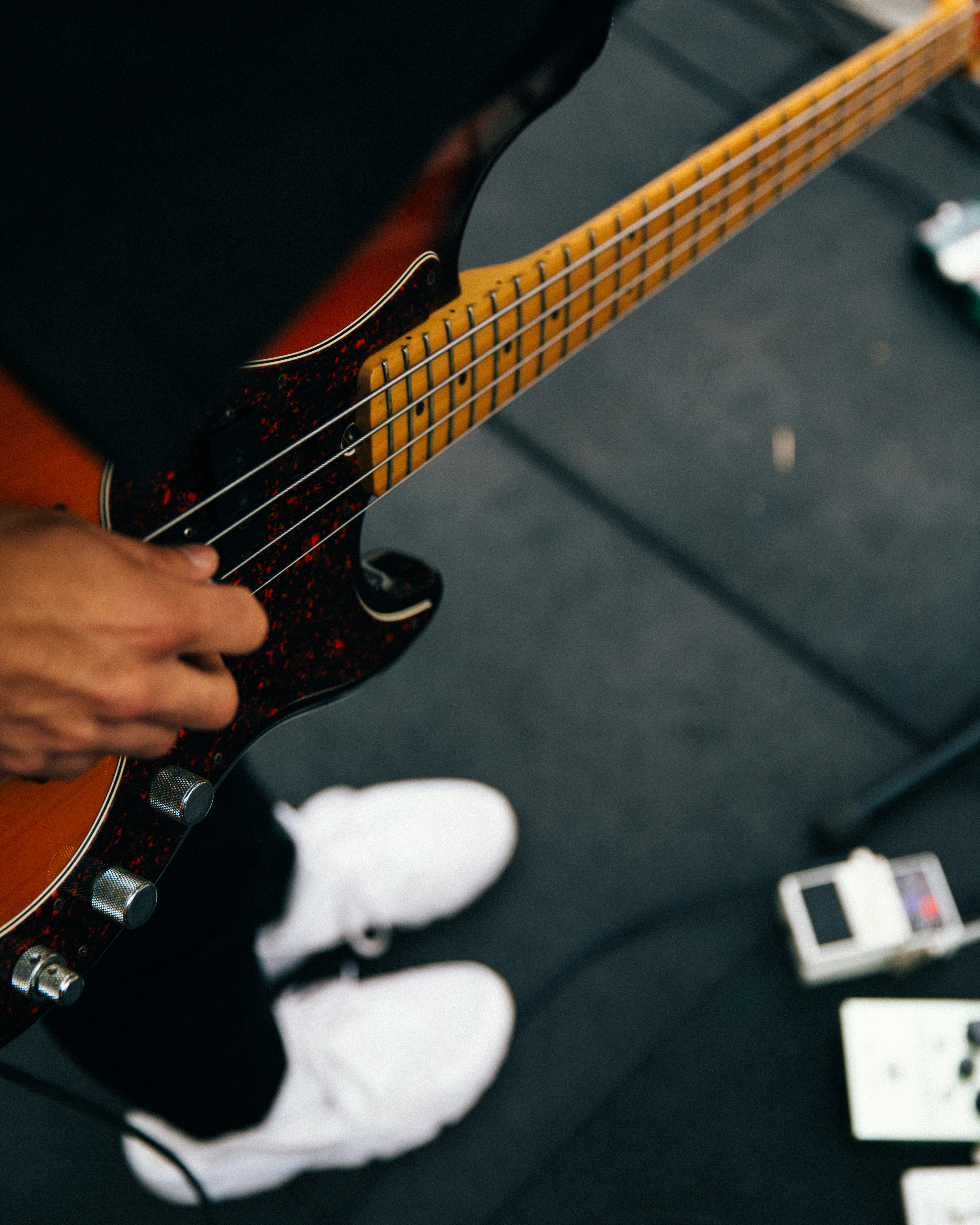 Close-up of a bassist's hand skillfully playing an electric bass guitar, with white sneakers visible below. The scene captures the essence of live music energy.