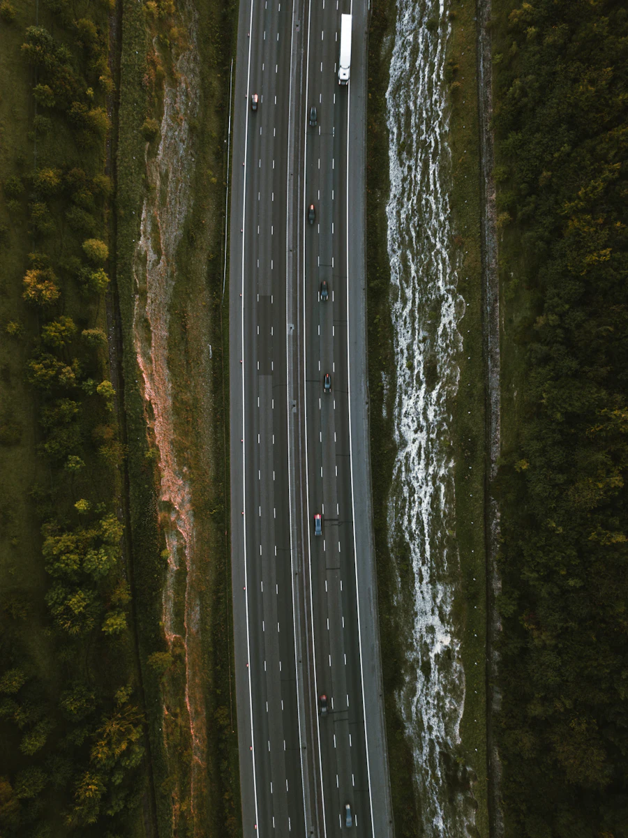 Top-down view of a divided highway cutting between dense forest and a snowy strip of ground, with a few vehicles traveling along the lanes.