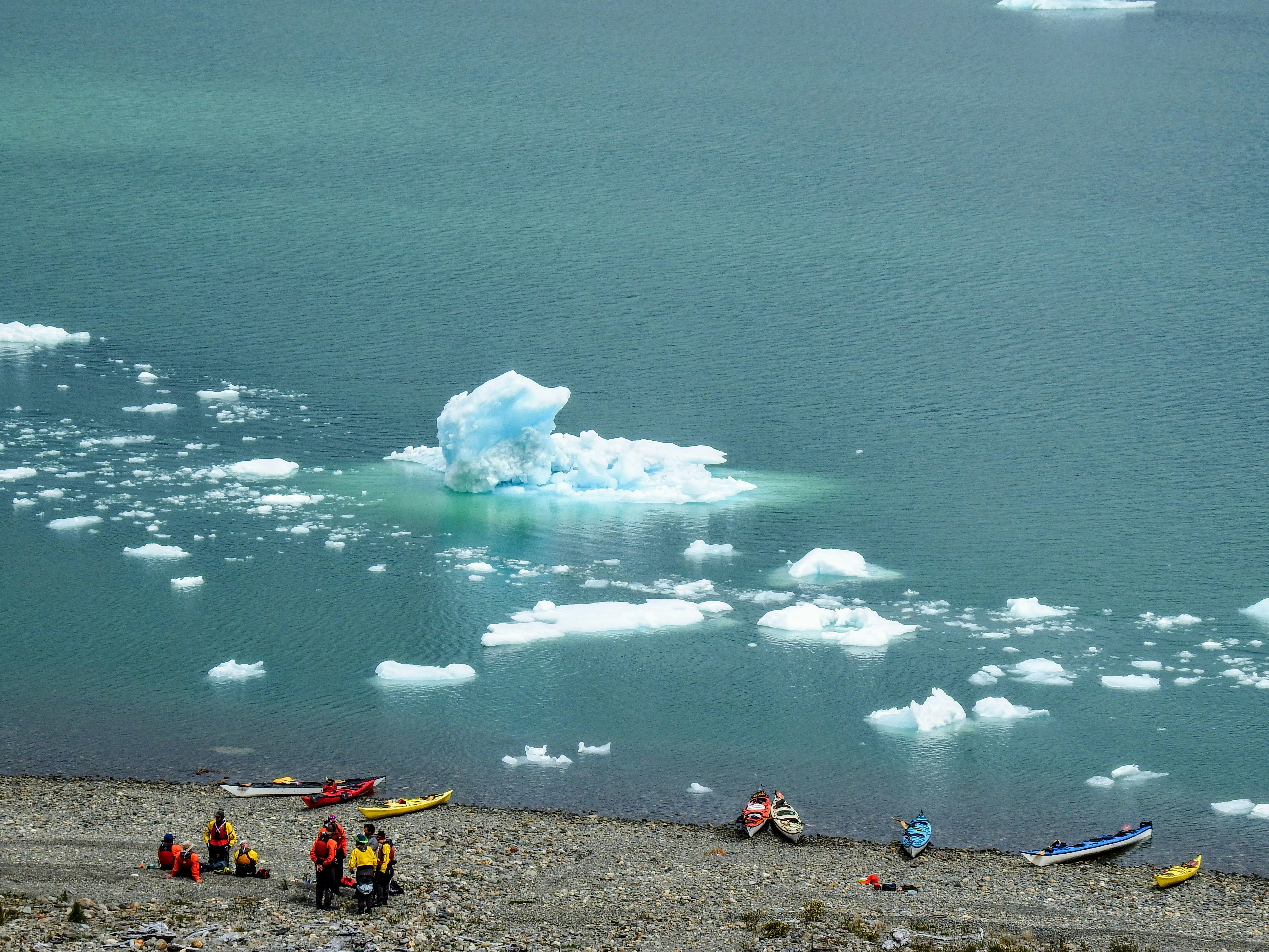 Temporarily blocked in by a wave of ice, we hung out on the shore of this remote island, a couple miles from base camp. Fear was not on our mind, we could only sense the solitude in this place. 

Watching from above as the expedition members mingled provided a calm, detached perspective, from which I could see the source of the crumbling ice. | people standing near seashore