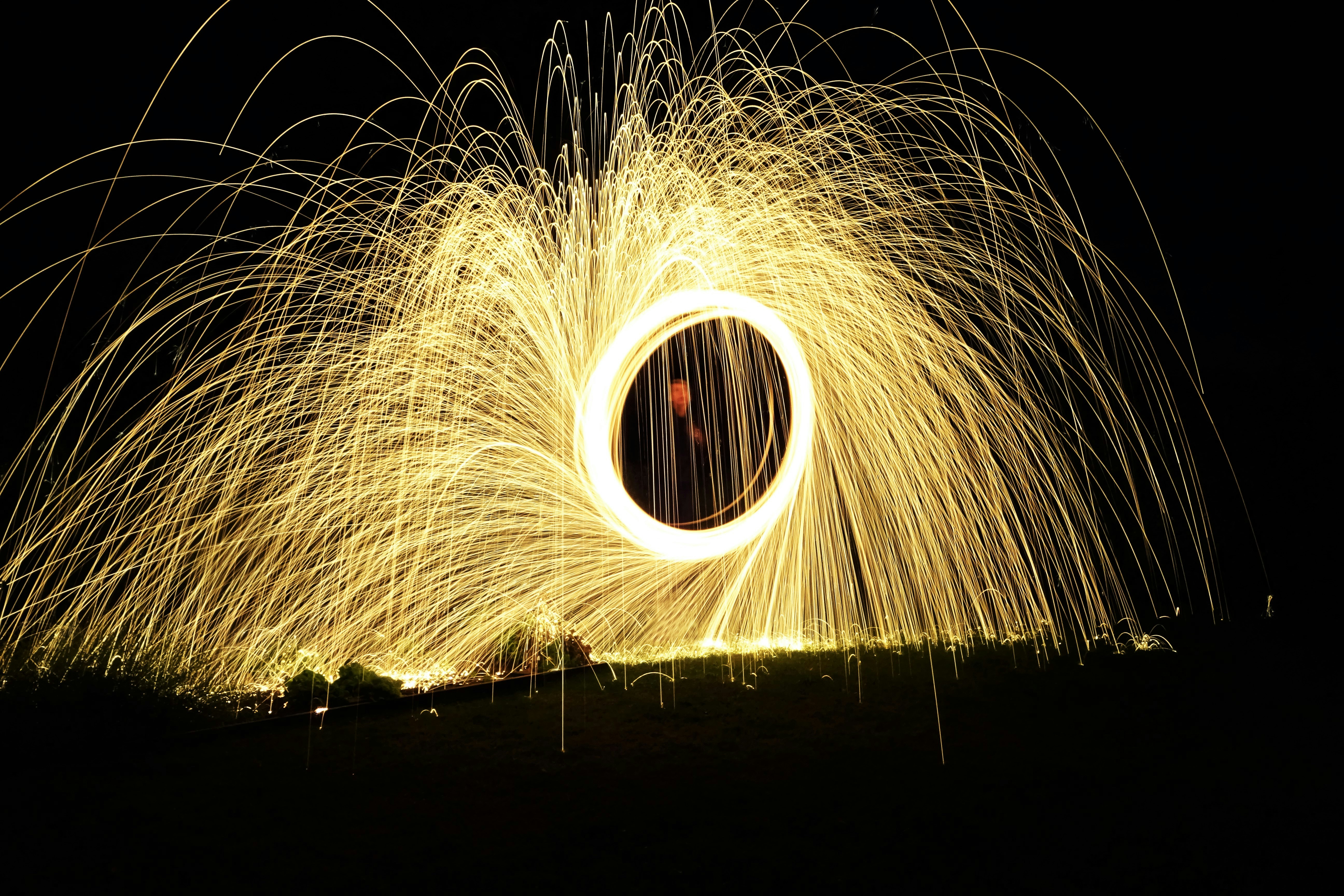 A circular pattern of fiery sparks radiating outward in a dark environment, creating a striking visual effect. The scene captures the dynamic motion of light in the night sky.
