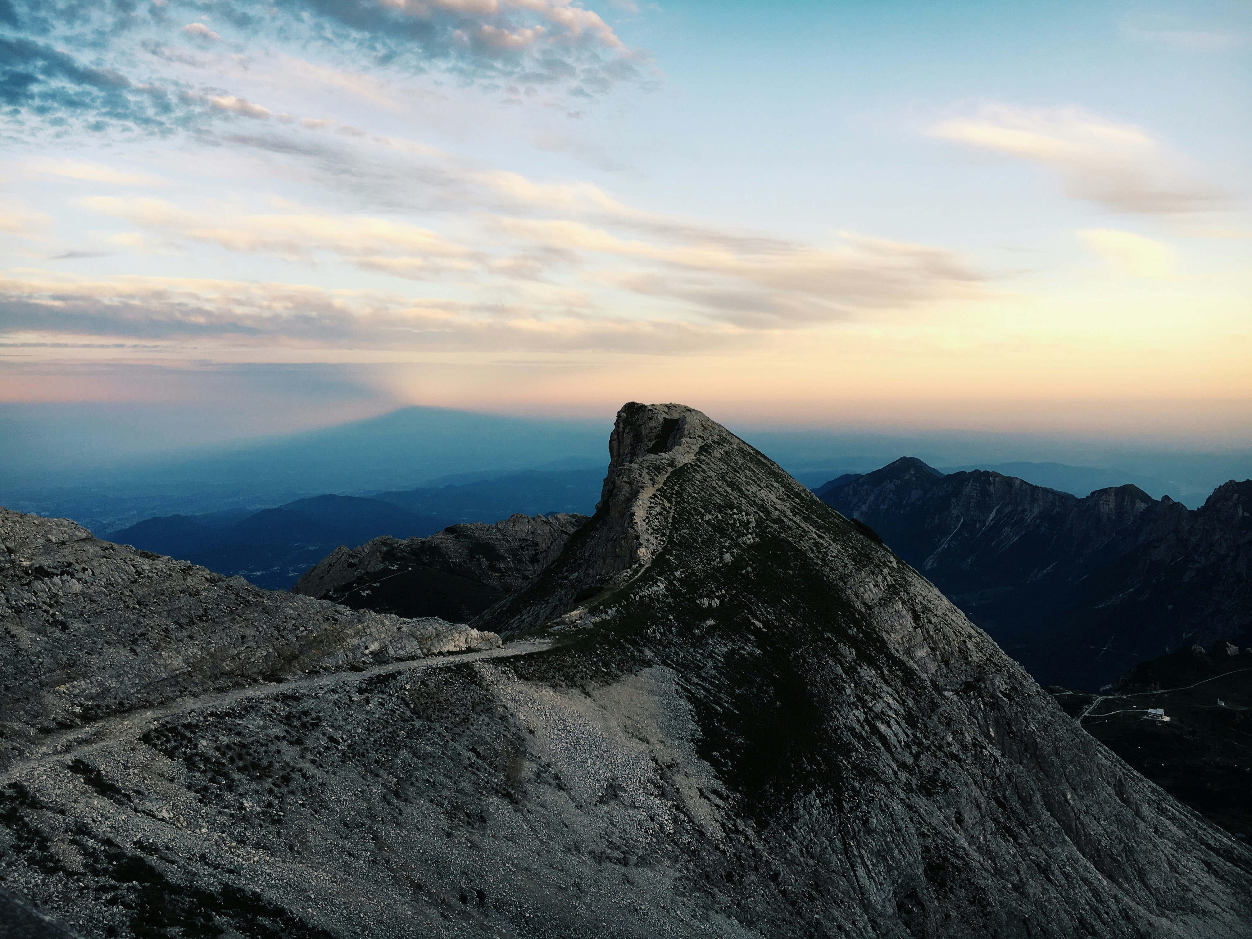 Dramatic mountain peak at dusk with a winding path under a colorful sky.