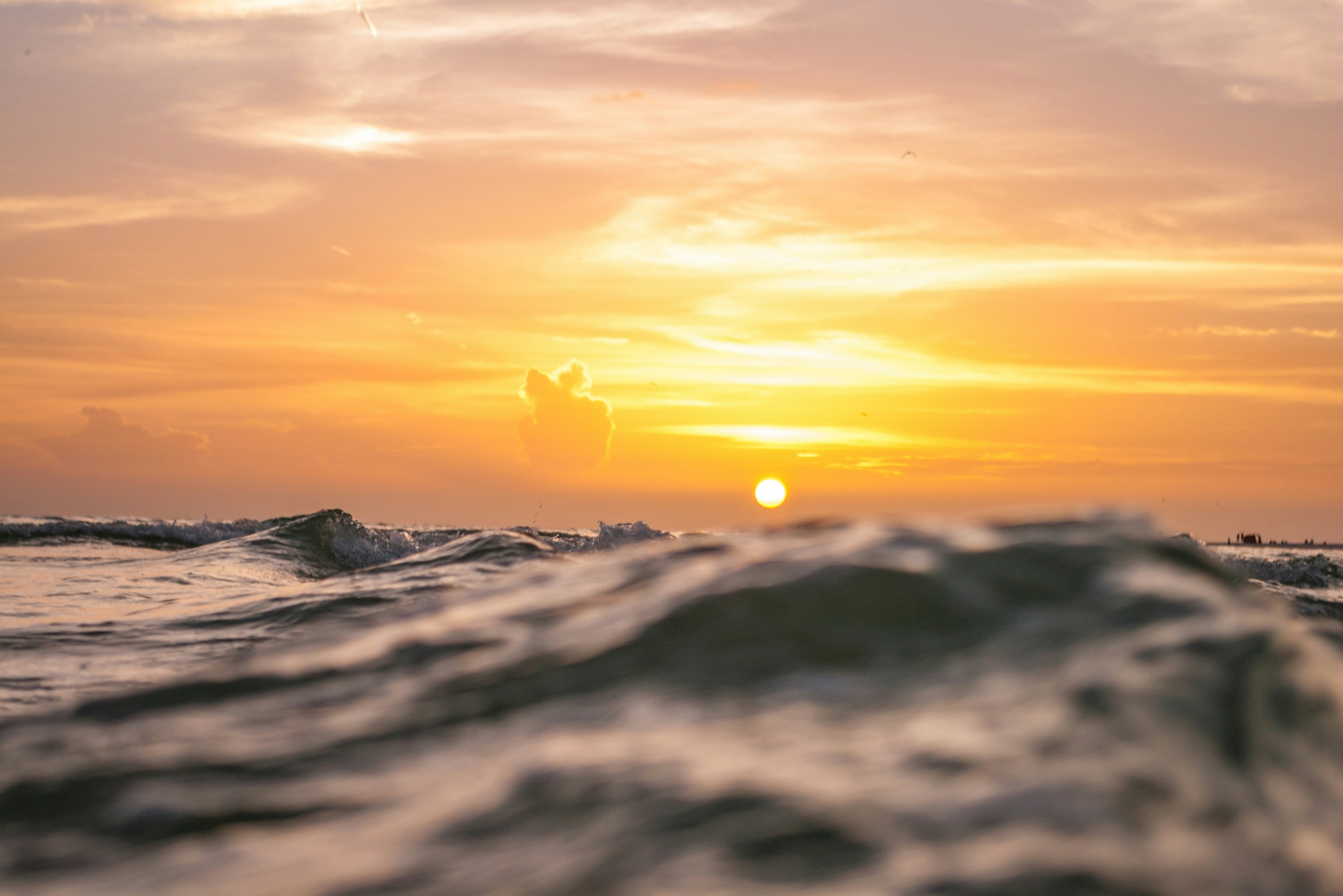 Waves in soft focus under a glowing orange sunset sky.