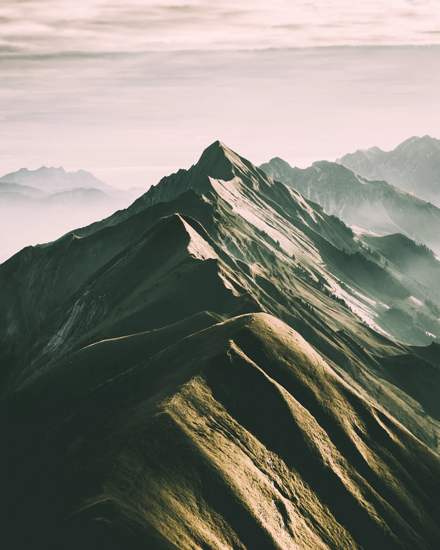 Sunlit mountain ridge with sharp peaks fading into misty layers under a pale sky.