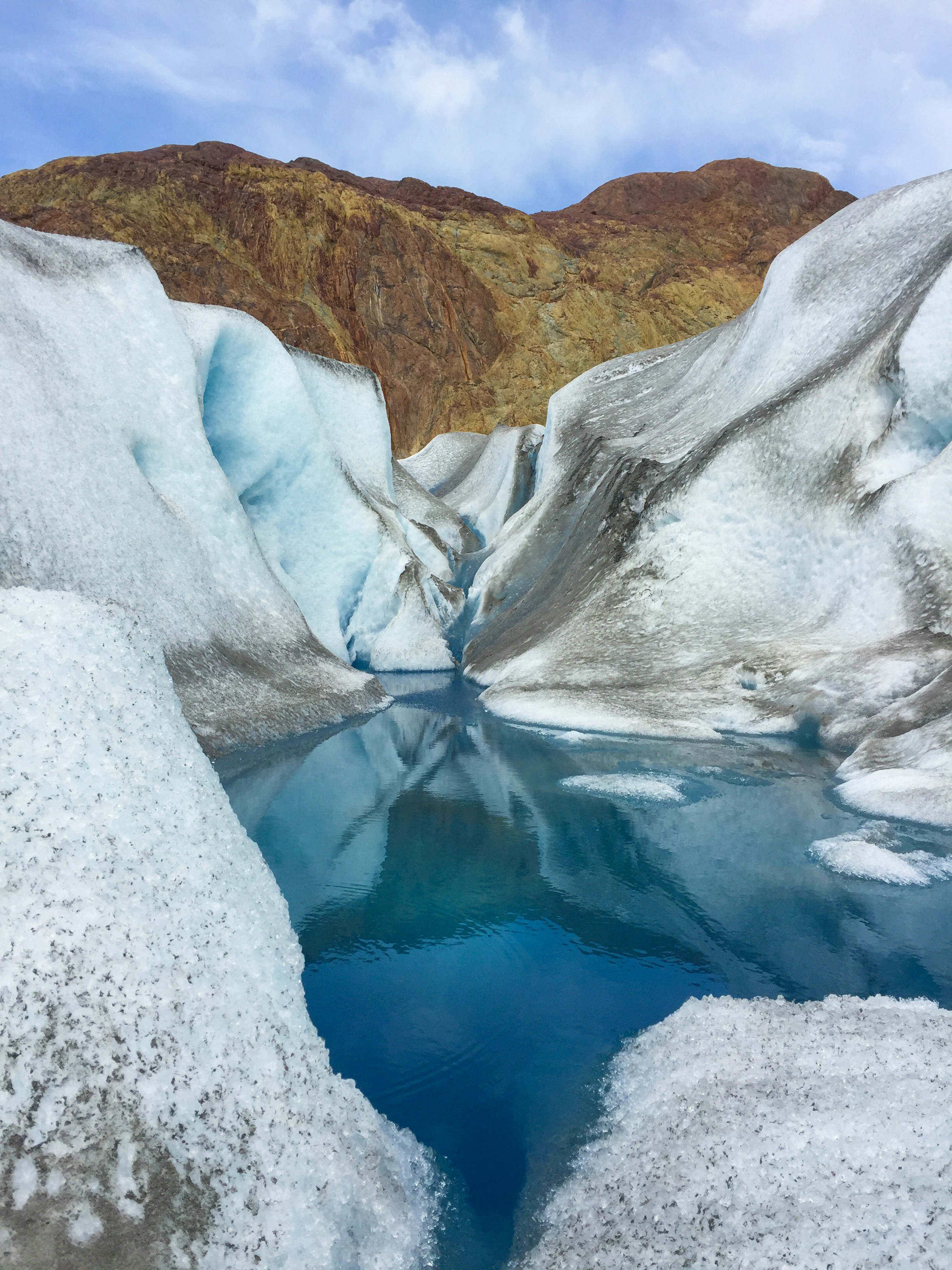 Pristine blue glacial pool nestled between rugged ice formations with a mountainous backdrop.