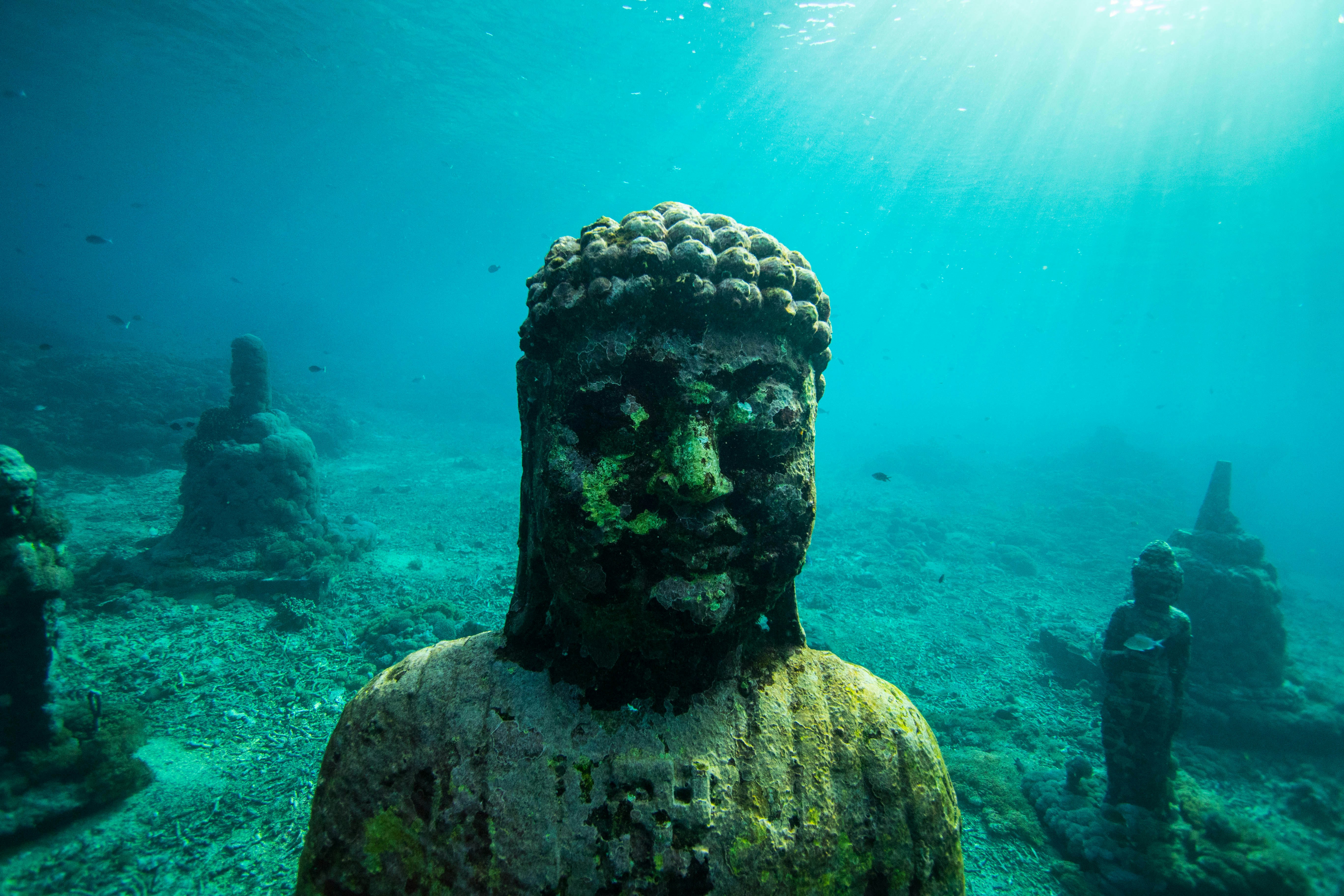 The closer you get to these statues the more detail you see and the more alive they feel. Behind these mossy eyes are detail, purpose, and touch of art. | human concrete statue deep in water