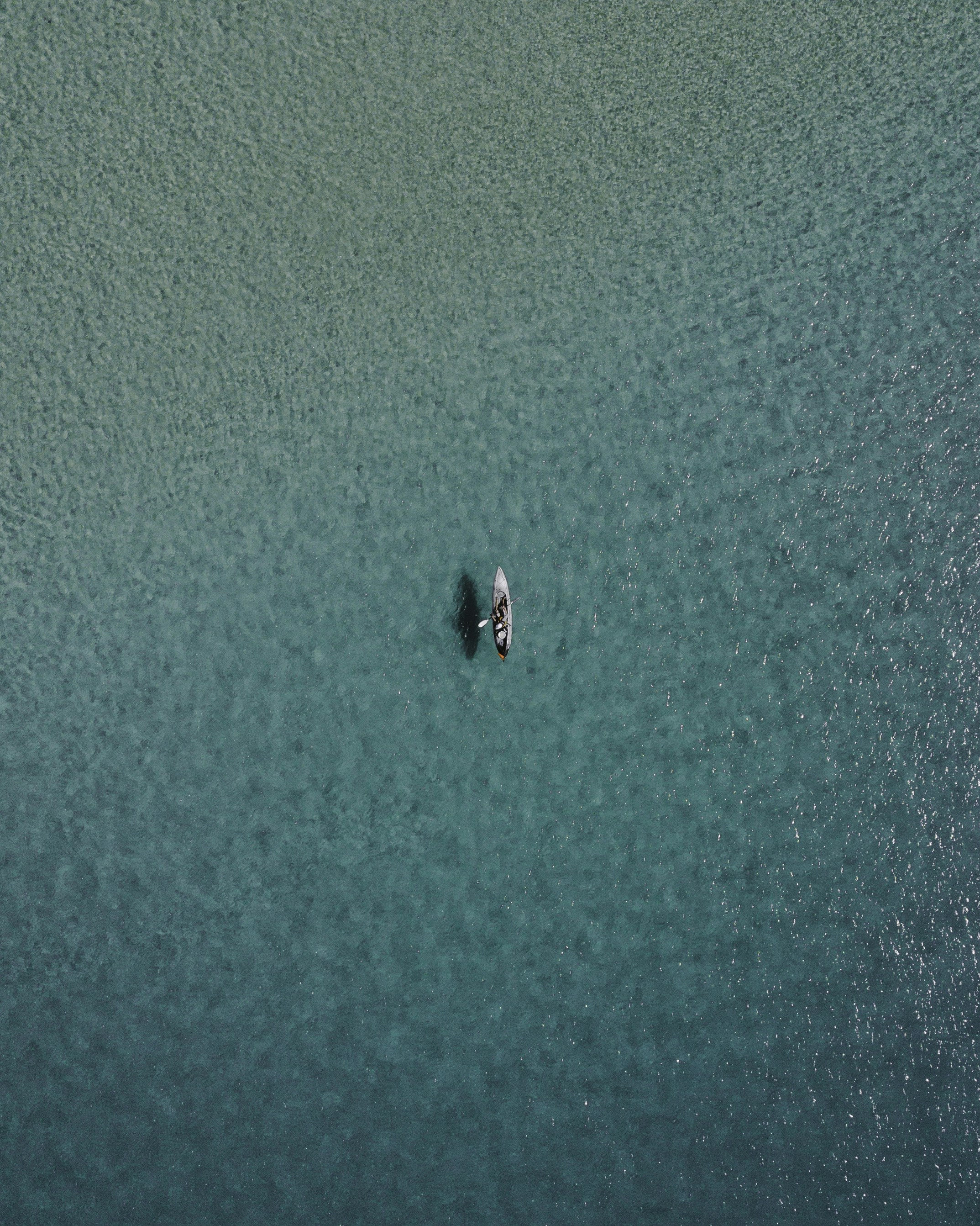 An ocean kayaker floats solo off shore in the sun watching the crystal blue waters below him. | white paddle boat on body of water