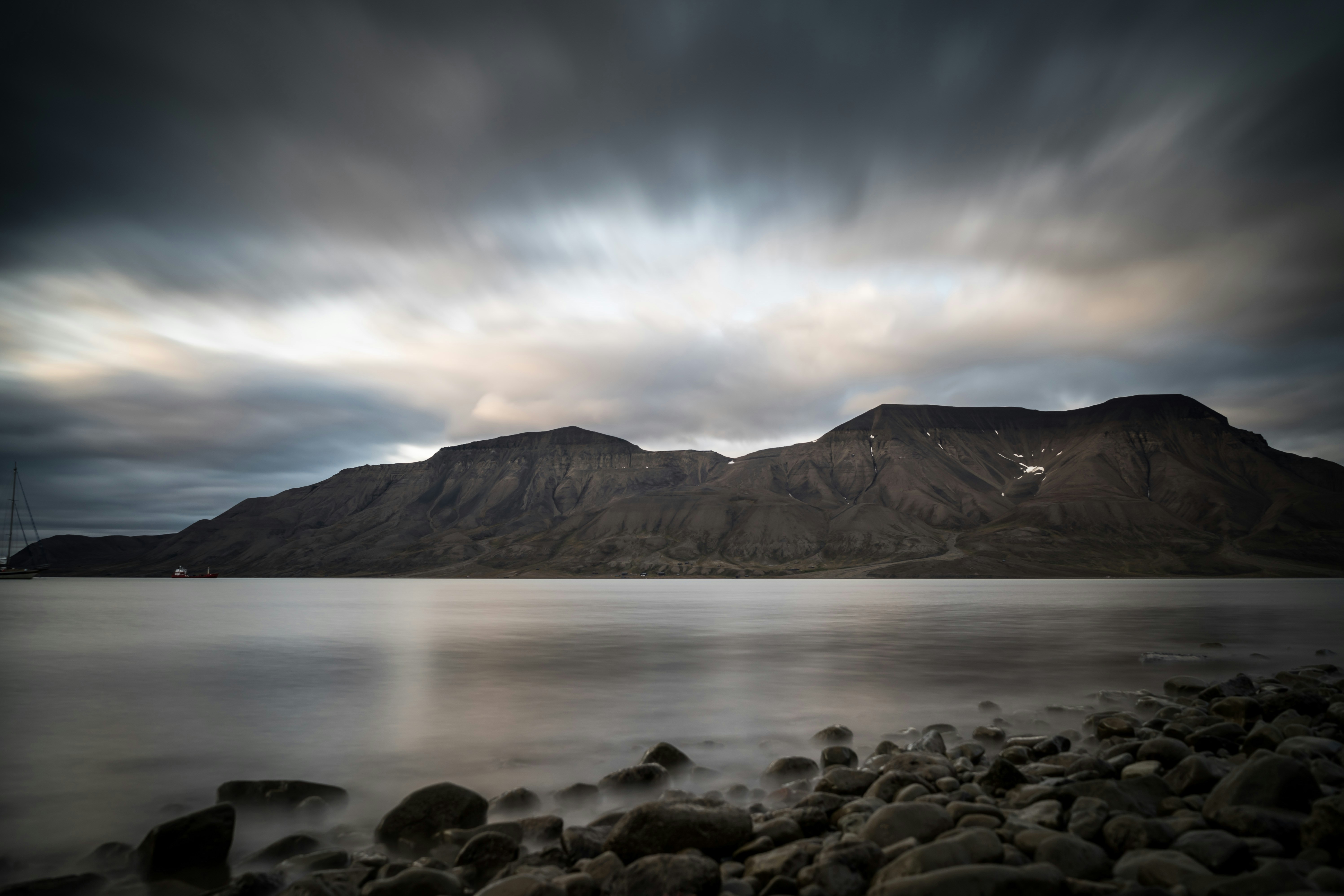 Long exposure of a serene mountain range reflecting on a calm lake beneath a dynamic sky.