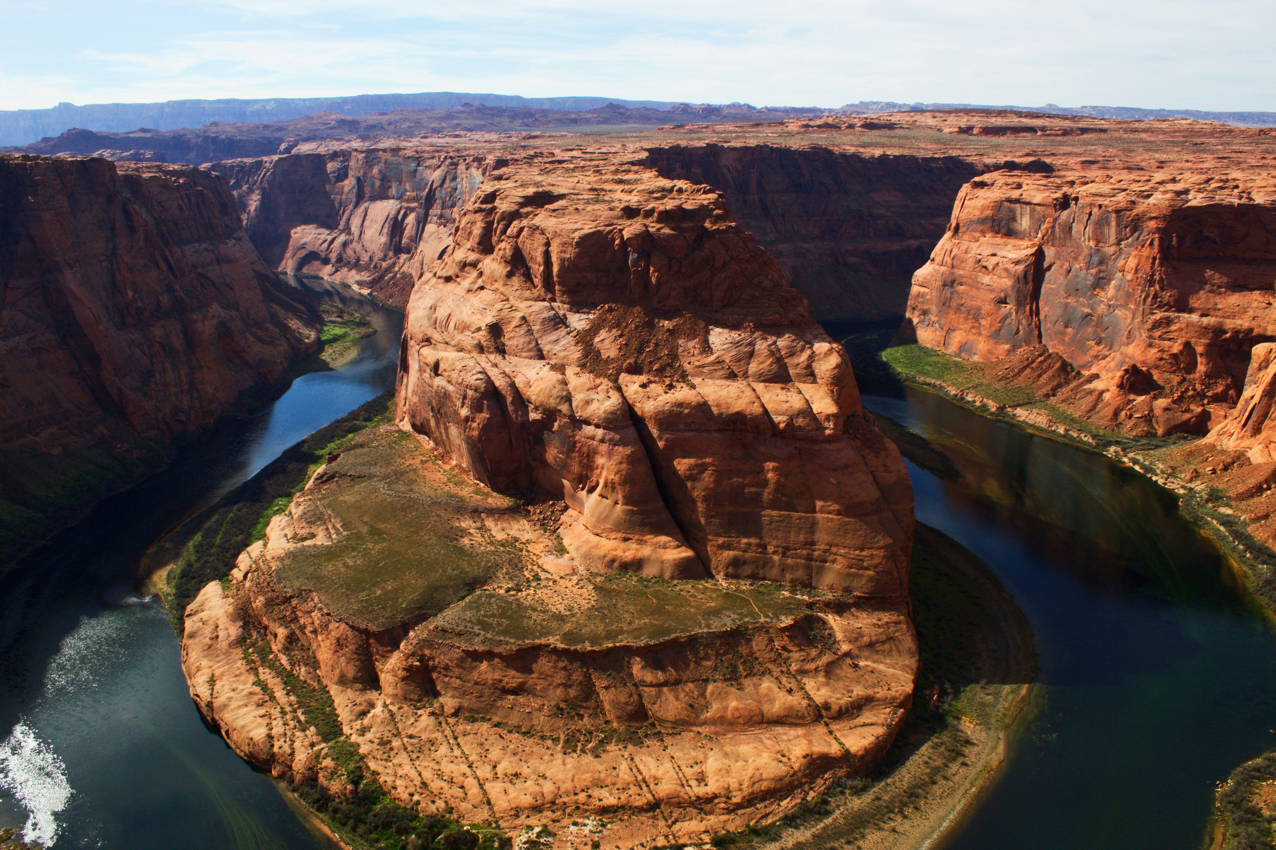 Panoramic view of the Horseshoe Bend with the Colorado River winding around the red rock formation under a clear blue sky.
