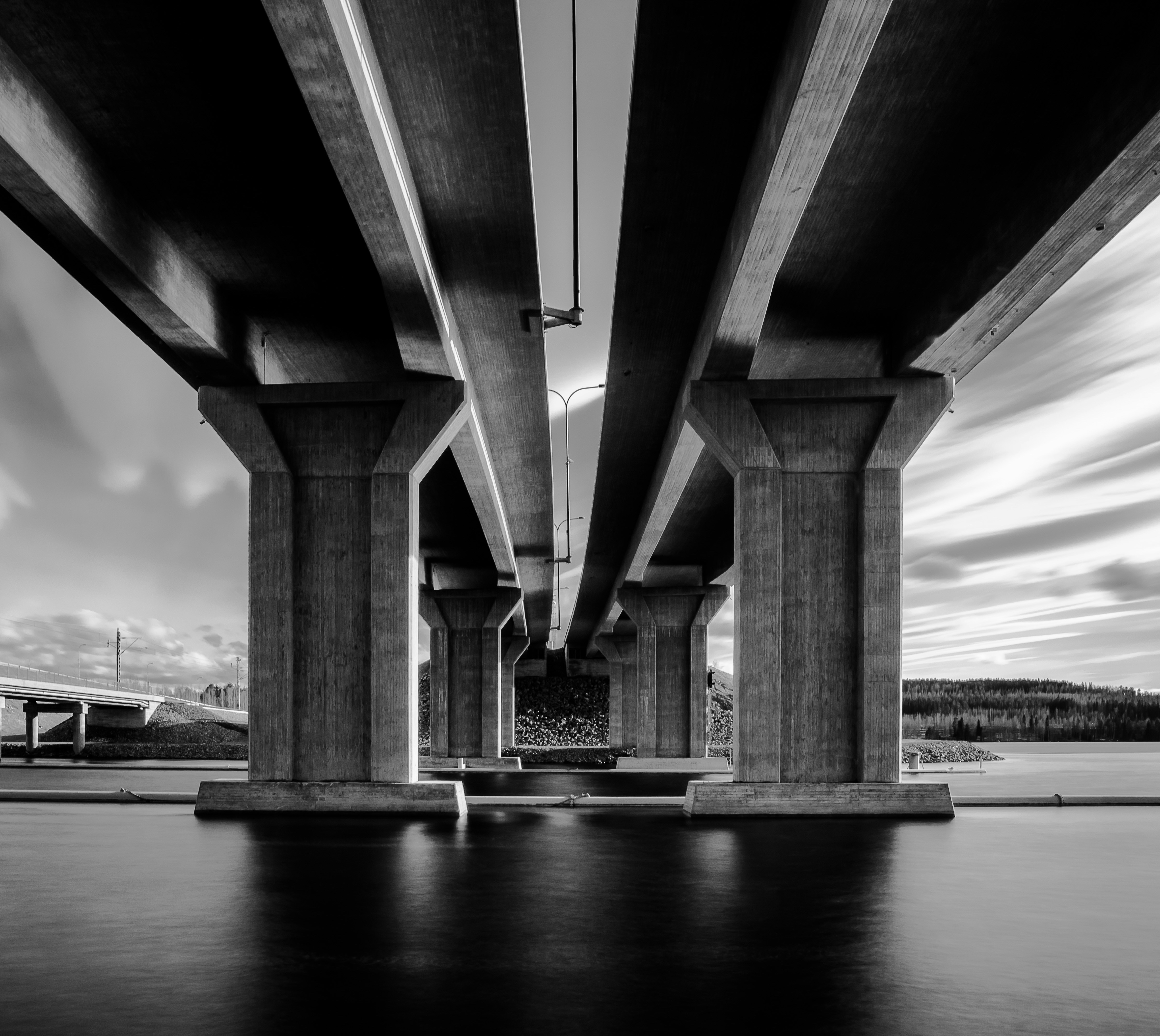 Dramatic grayscale view of a concrete bridge's underside, showcasing symmetrical lines and textures.