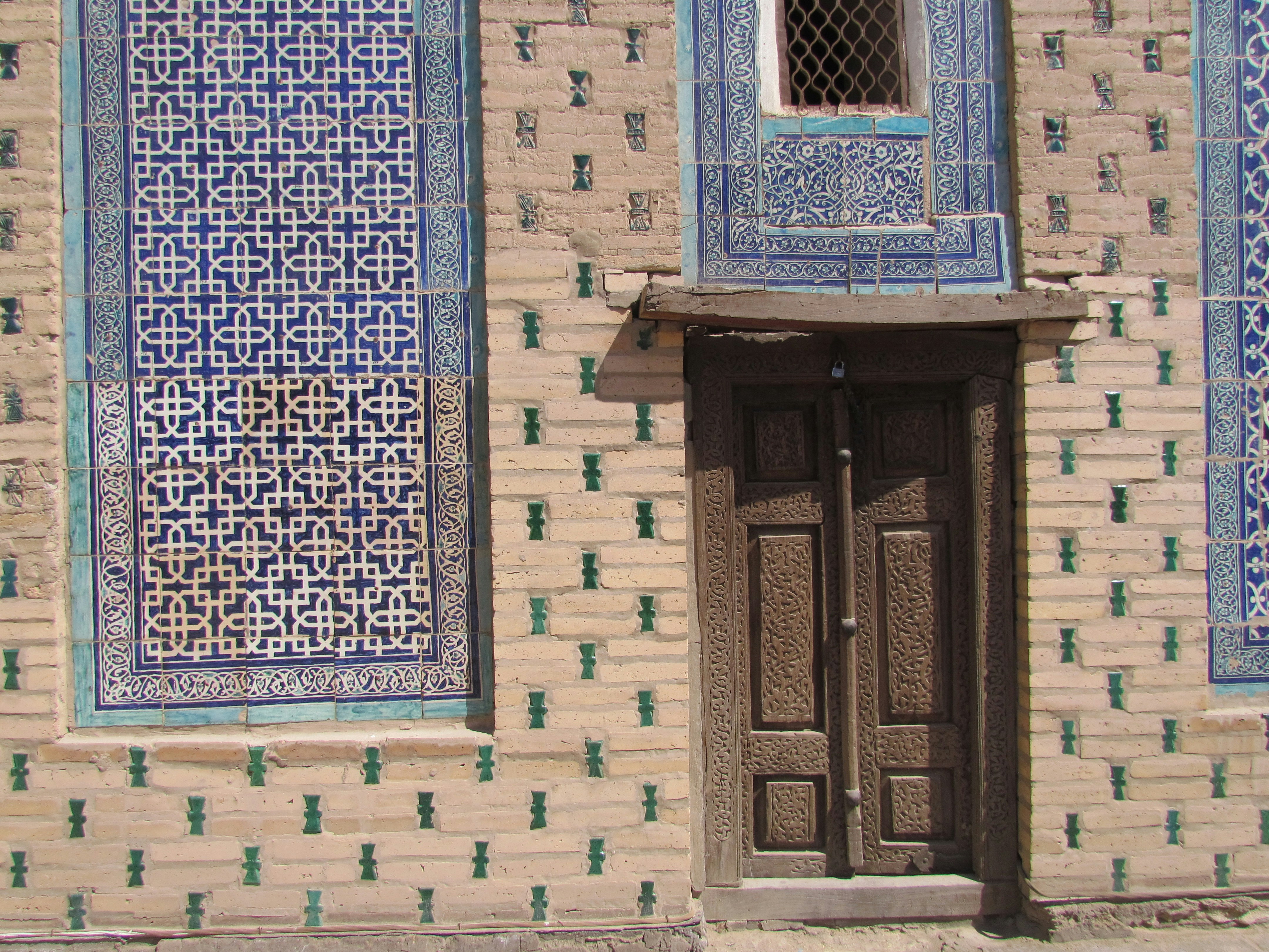 Ornate wooden door set within a vibrant blue and brown tiled wall, showcasing intricate geometric patterns.