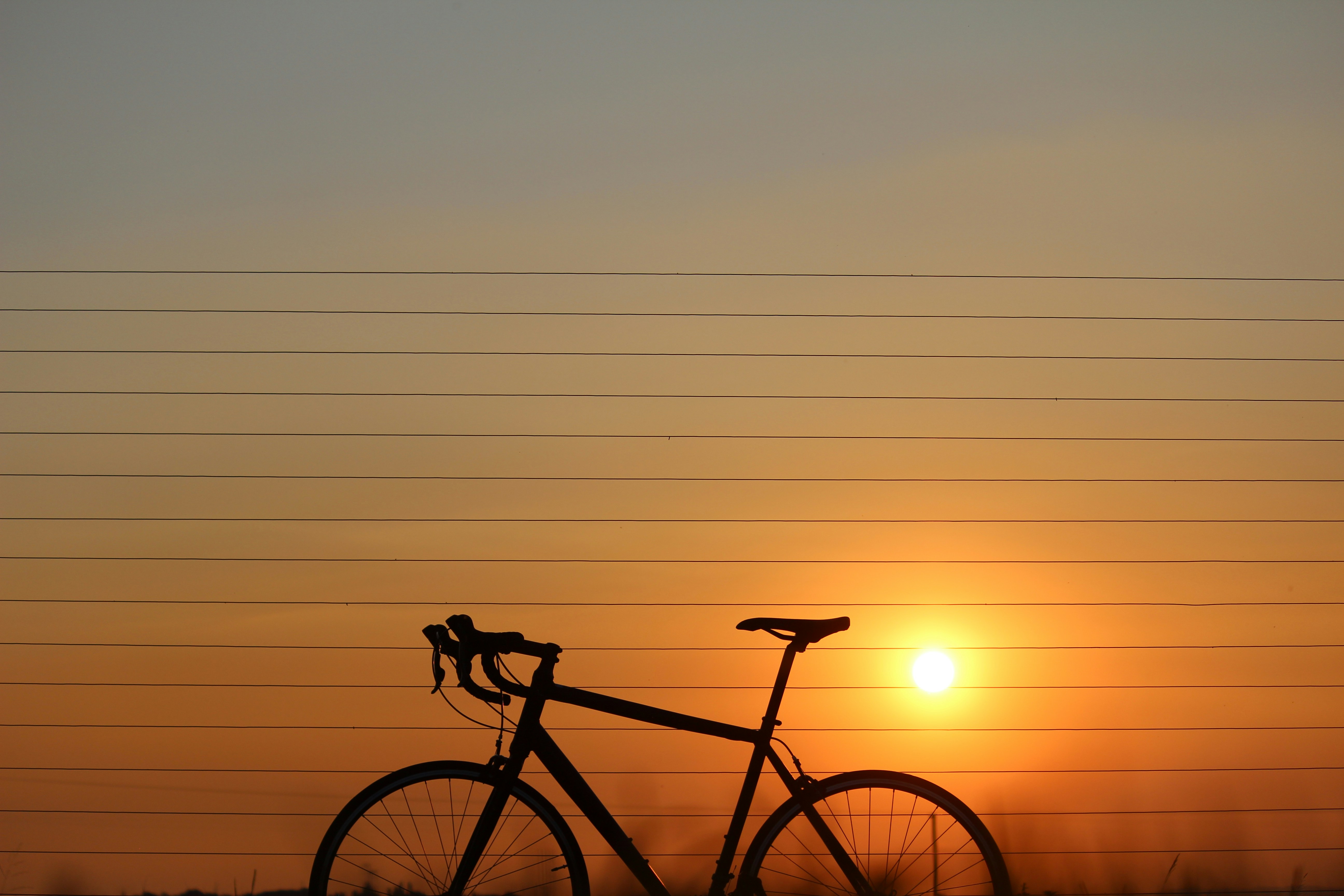 Silhouette of a bicycle against a vivid sunset sky with an orange sun near the horizon.
