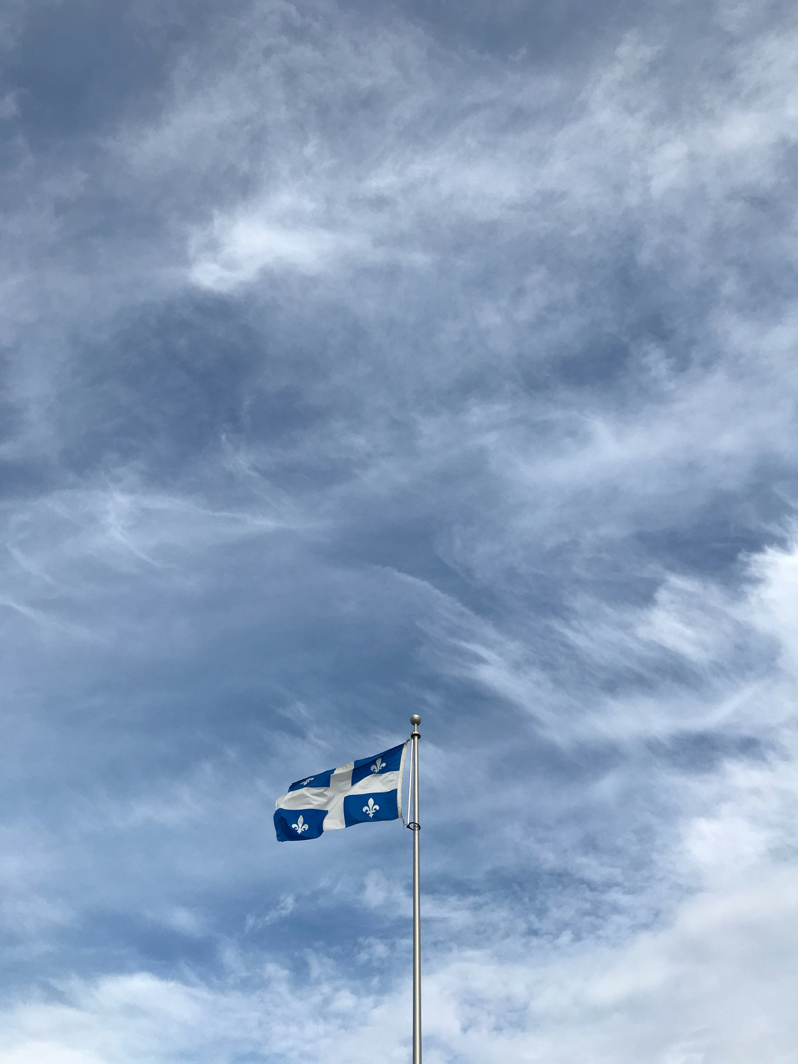 Quebec flag fluttering gently on a flagpole, set against a backdrop of wispy clouds and a blue sky.