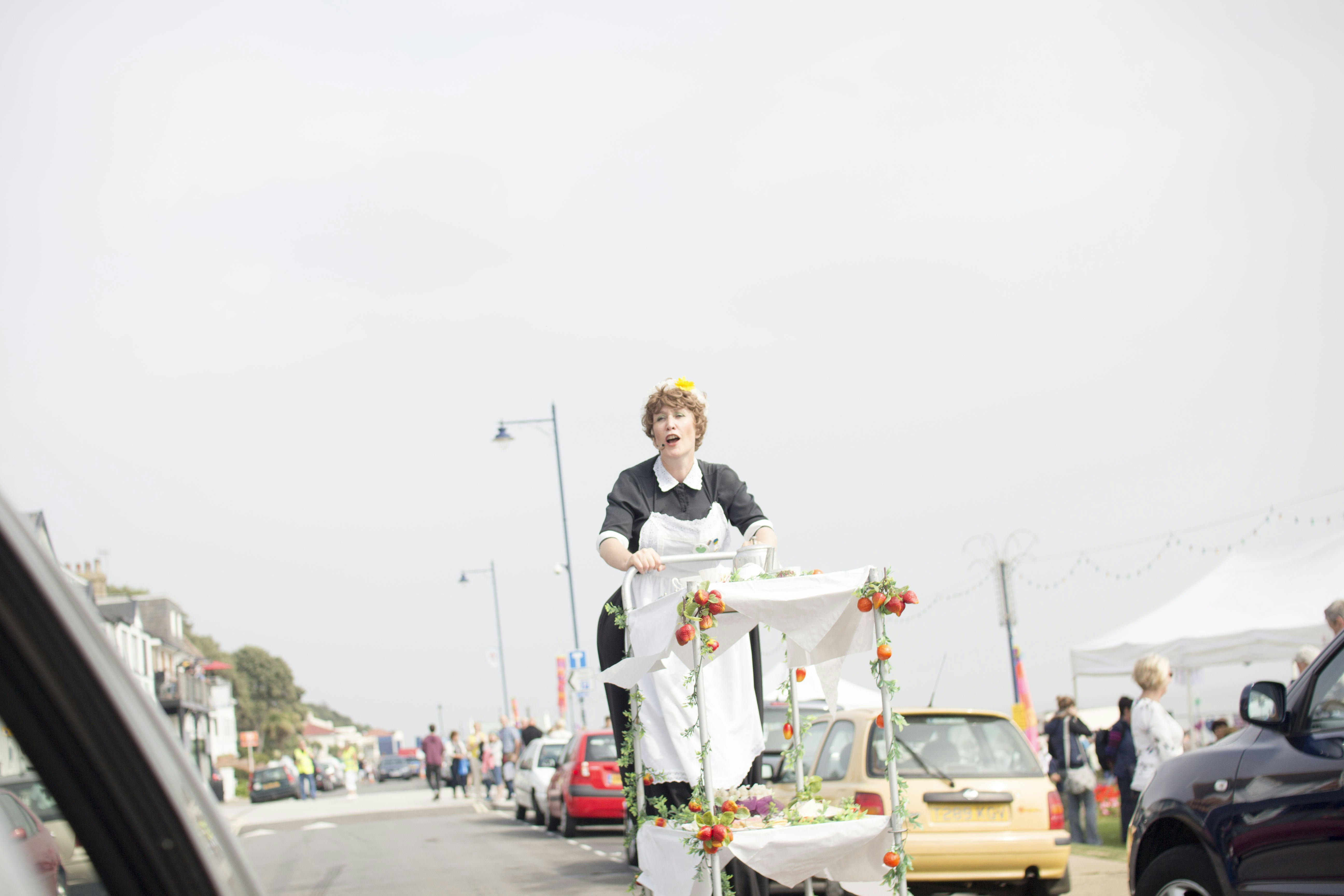 A performer dressed in traditional attire pushes a decorated cart along a bustling street during a local festival. The scene captures a lively community atmosphere.