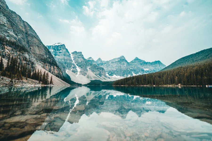 Turquoise alpine lake reflecting rugged snow-dusted mountains and a pine-lined shore beneath a bright sky.