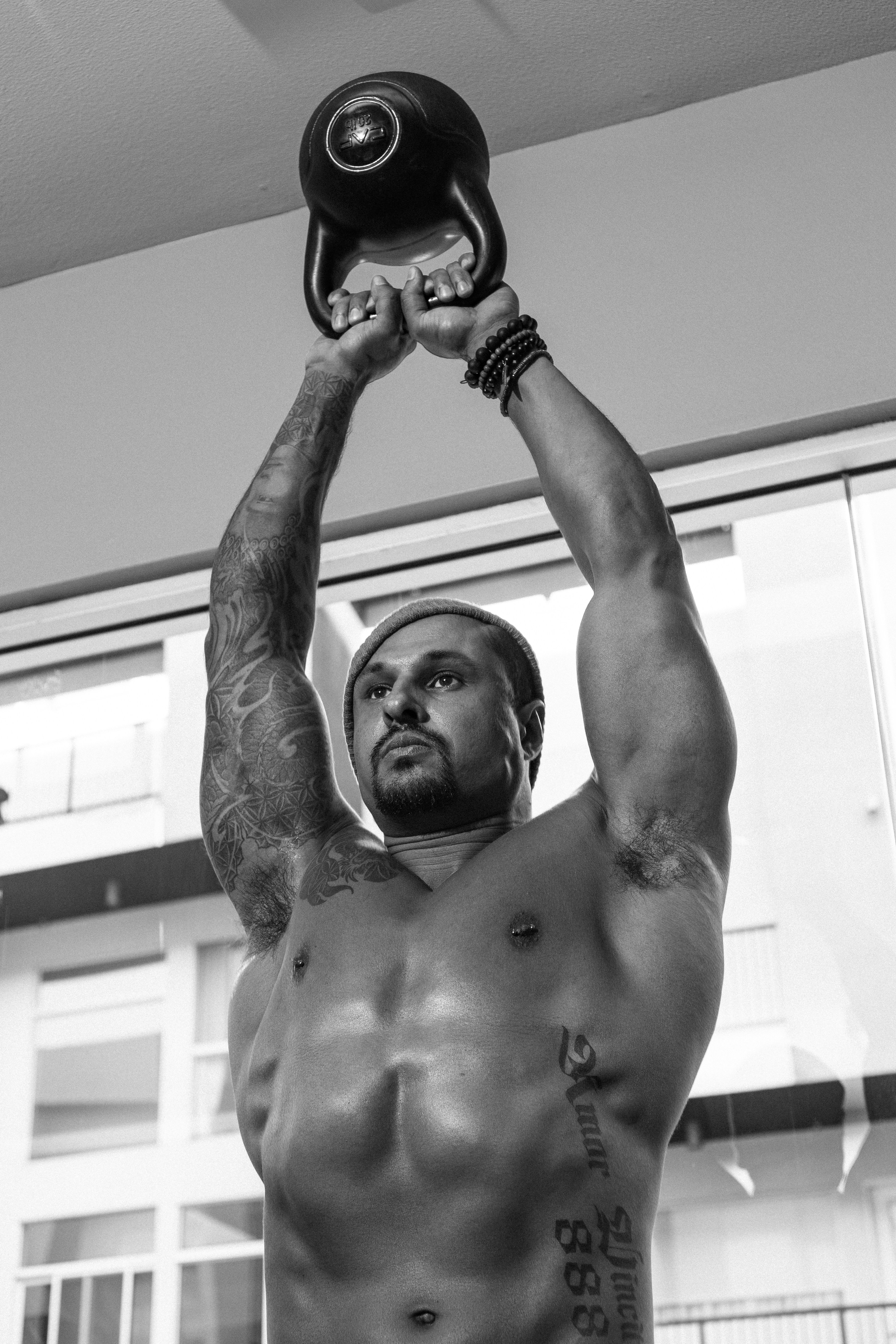 Muscular man performing a kettlebell lift in a gym, showcasing strength and focus. The monochrome effect emphasizes the intensity of the workout.
