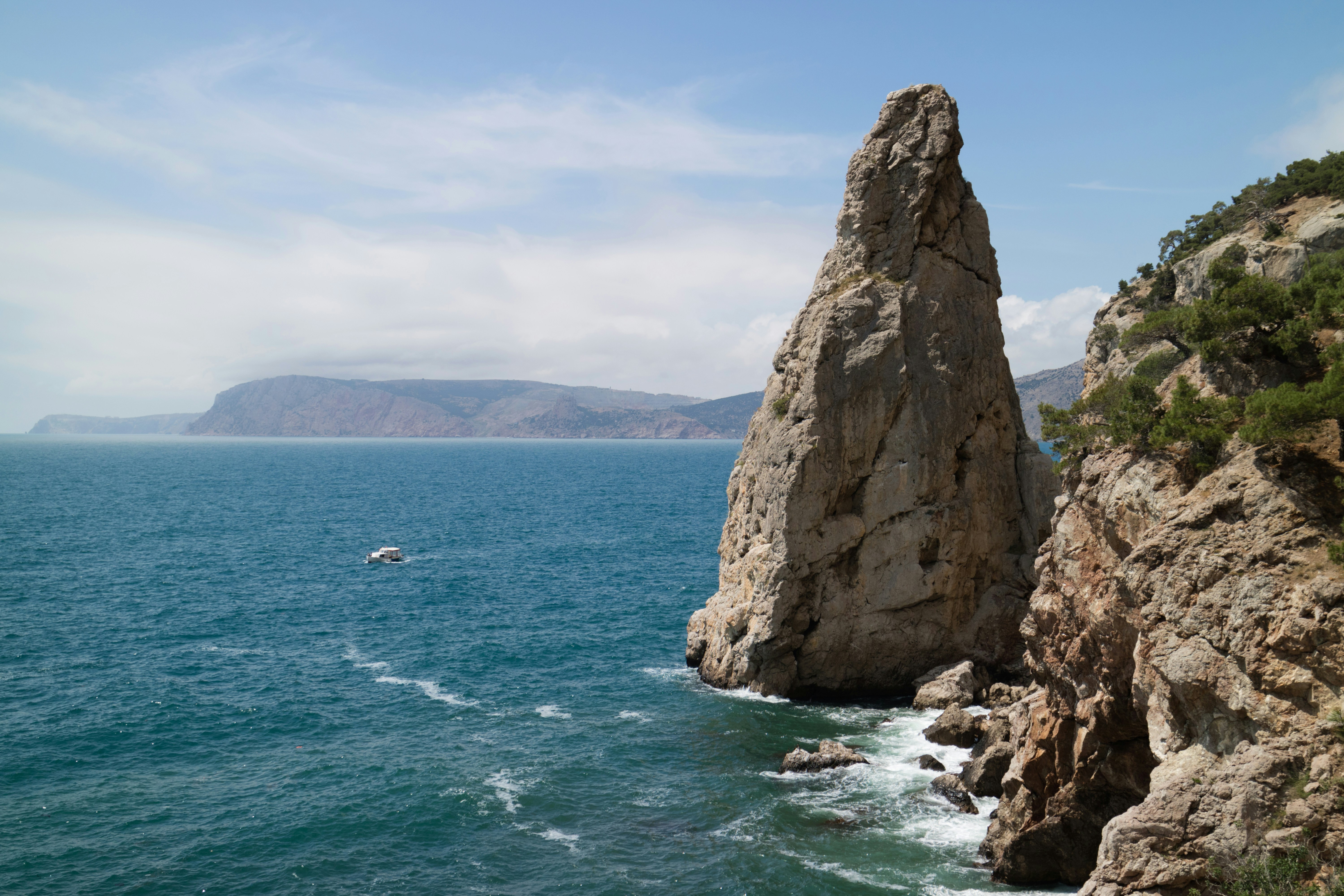 A towering rock formation stands proudly against a vibrant sea, with distant hills framing the horizon. The scene captures the rugged beauty of coastal landscapes.