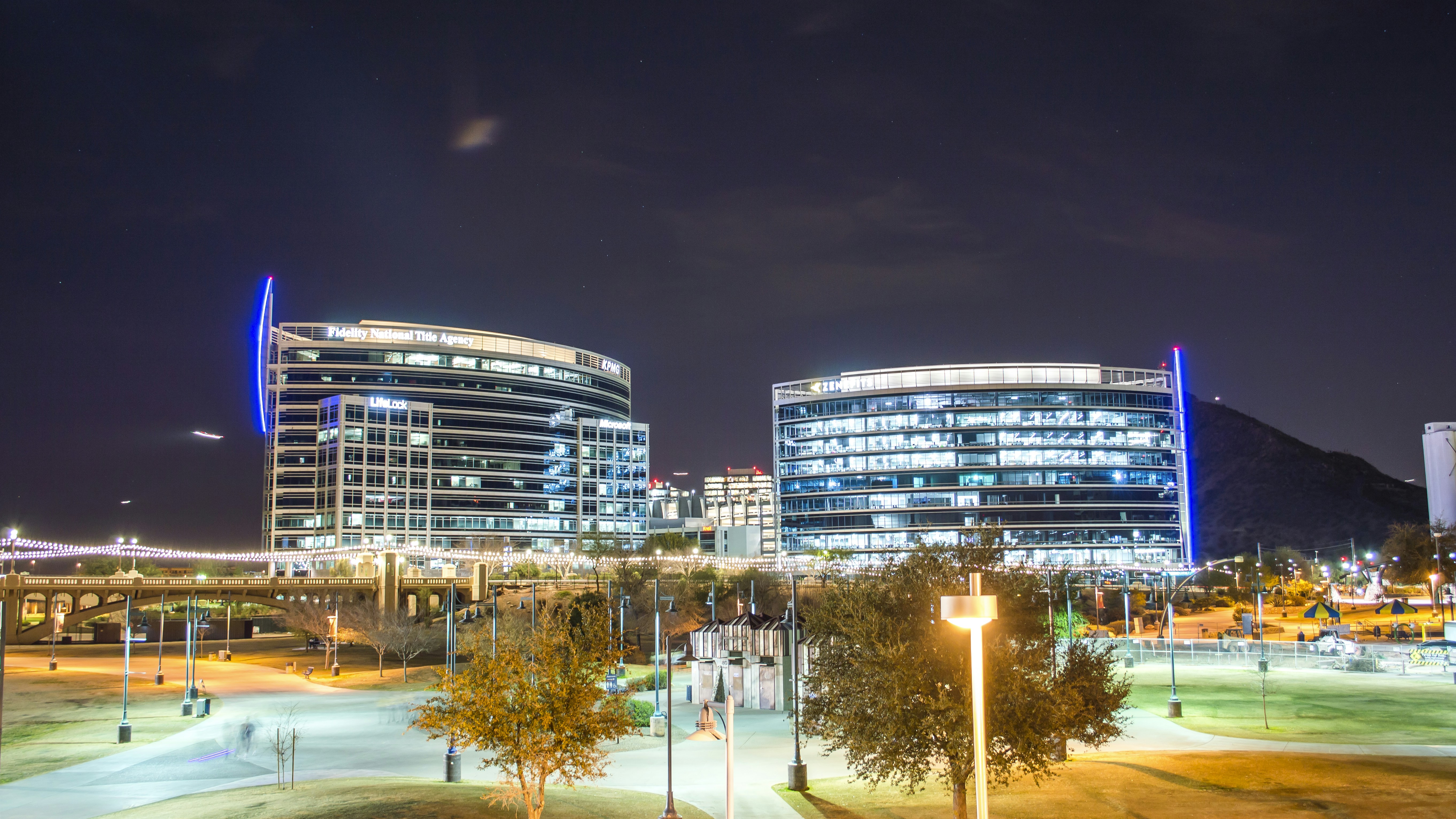 Two contemporary office buildings illuminated against a night sky, showcasing architectural design and urban life. The scene captures the essence of a bustling city environment.