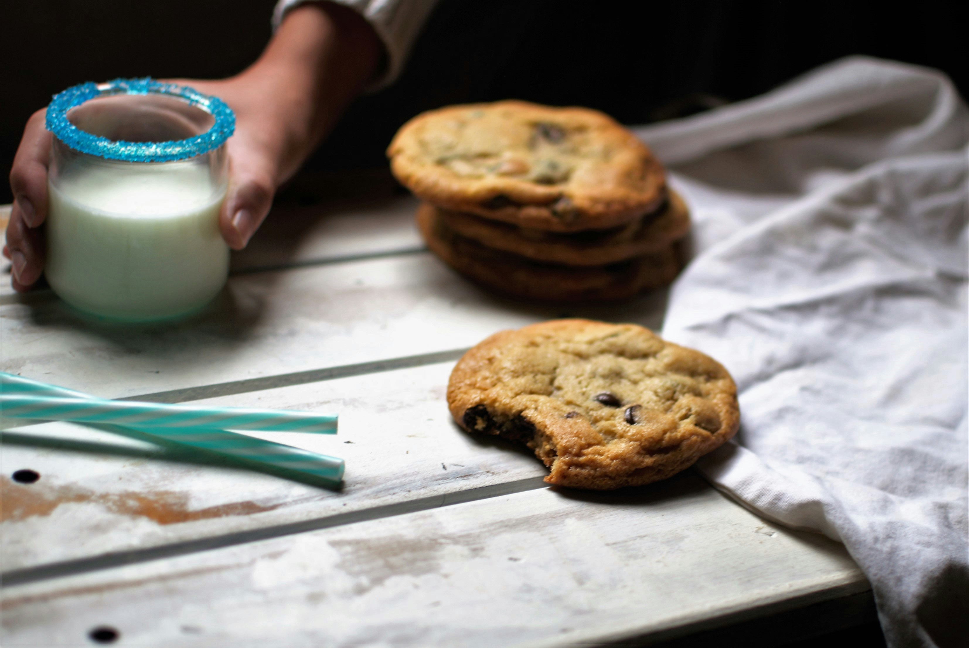 Homemade chocolate chip cookies paired with a glass of milk, set on a rustic wooden table. A playful touch with colorful straws adds to the inviting scene.