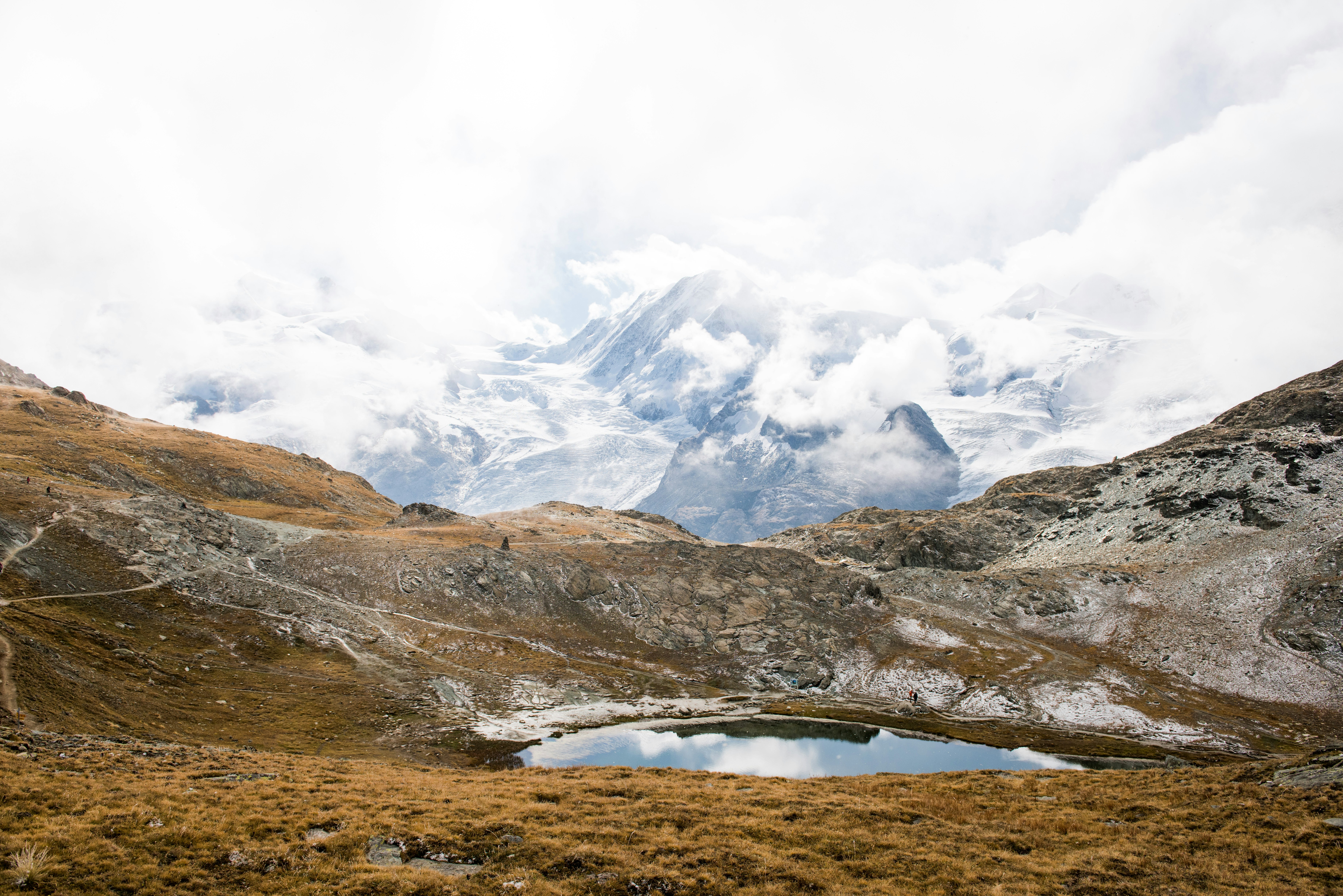 A serene alpine landscape featuring a tranquil lake surrounded by rugged mountain terrain under a blanket of clouds.
