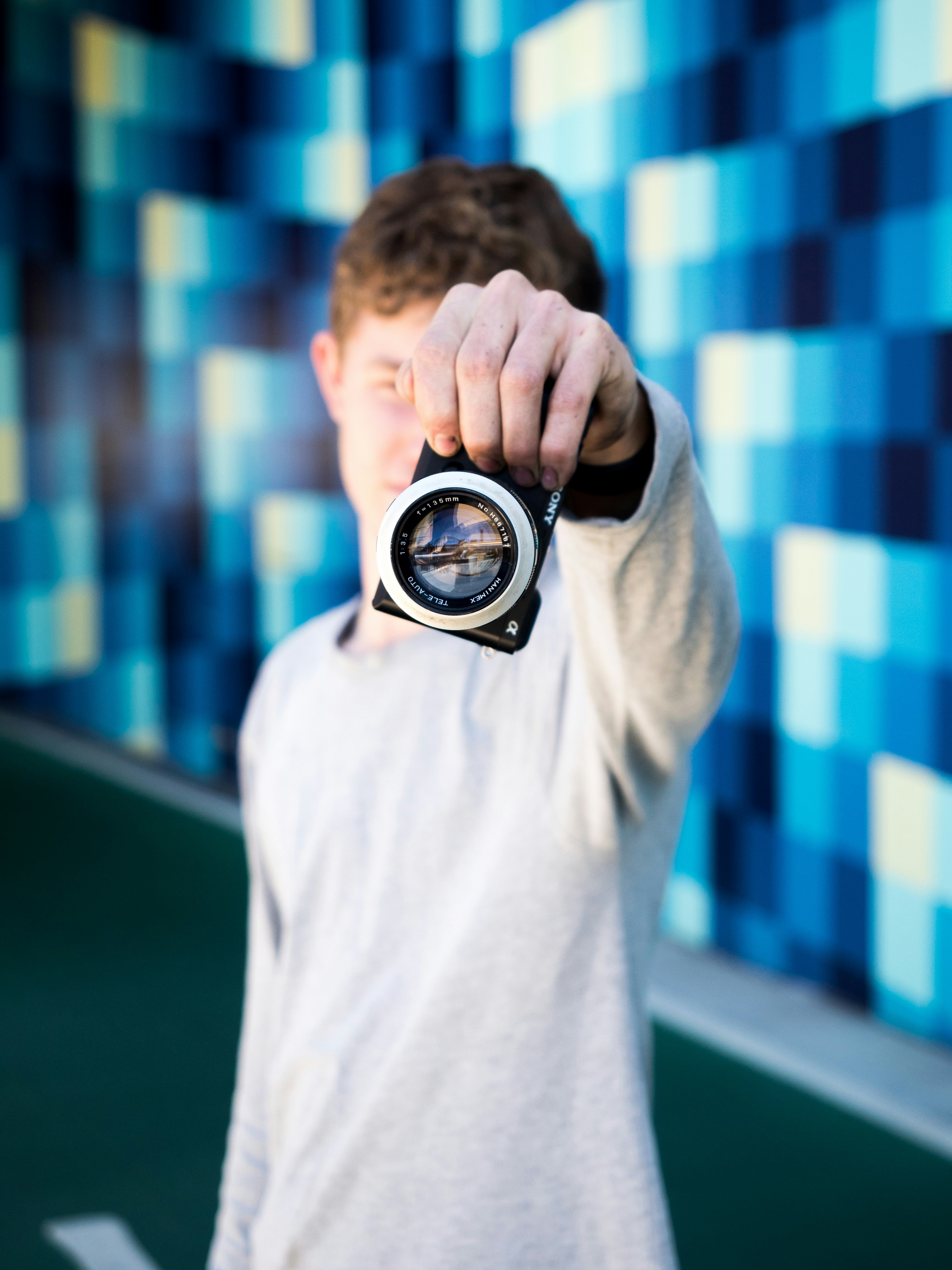 A young man holds a camera in front of him, showcasing his passion for photography against a vibrant, geometric background.