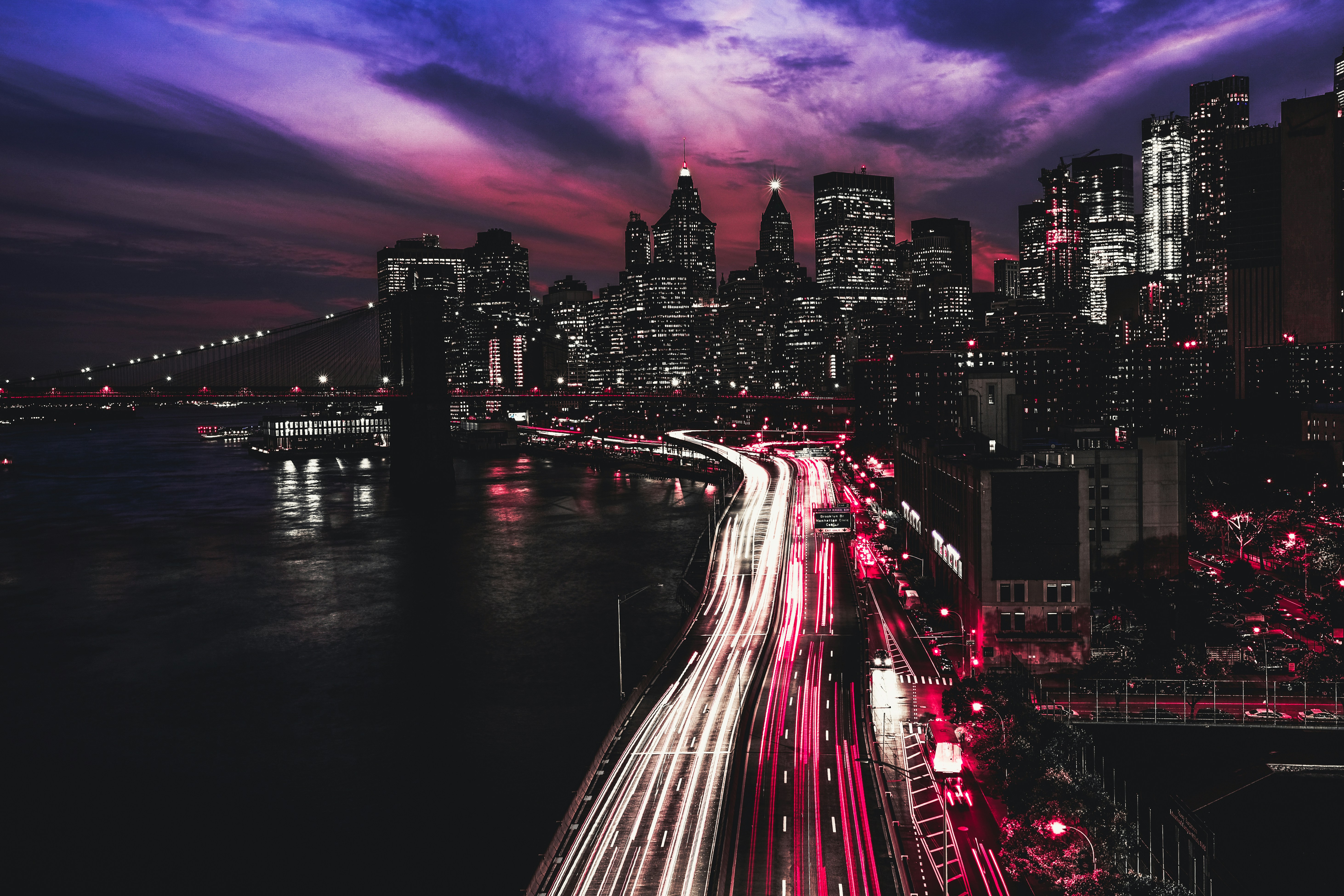 City skyline with illuminated skyscrapers and light trails from traffic under a dramatic purple sky.