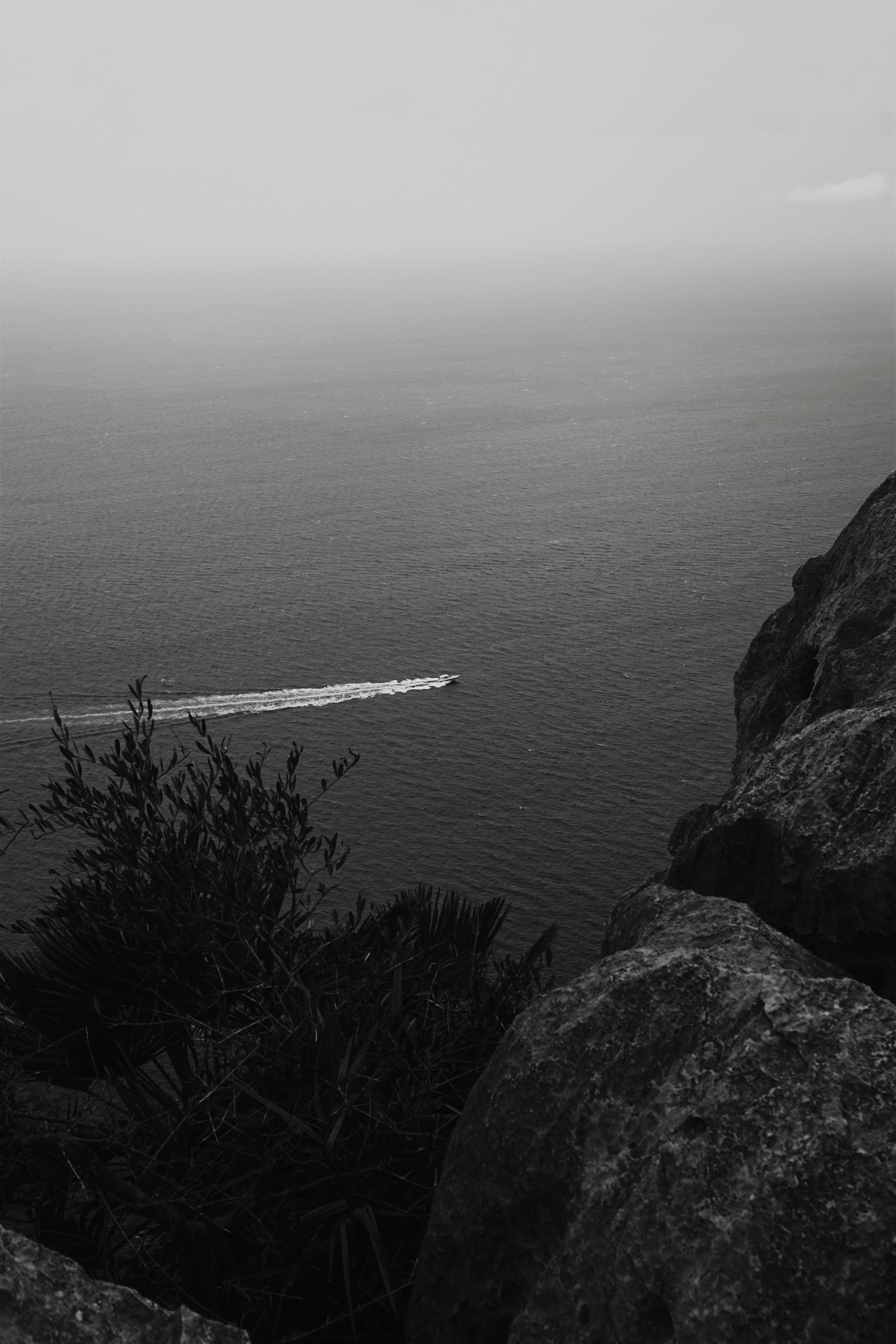 Monochrome Wake: A Lone Boat Traces a White Line Past Rugged Cliffs