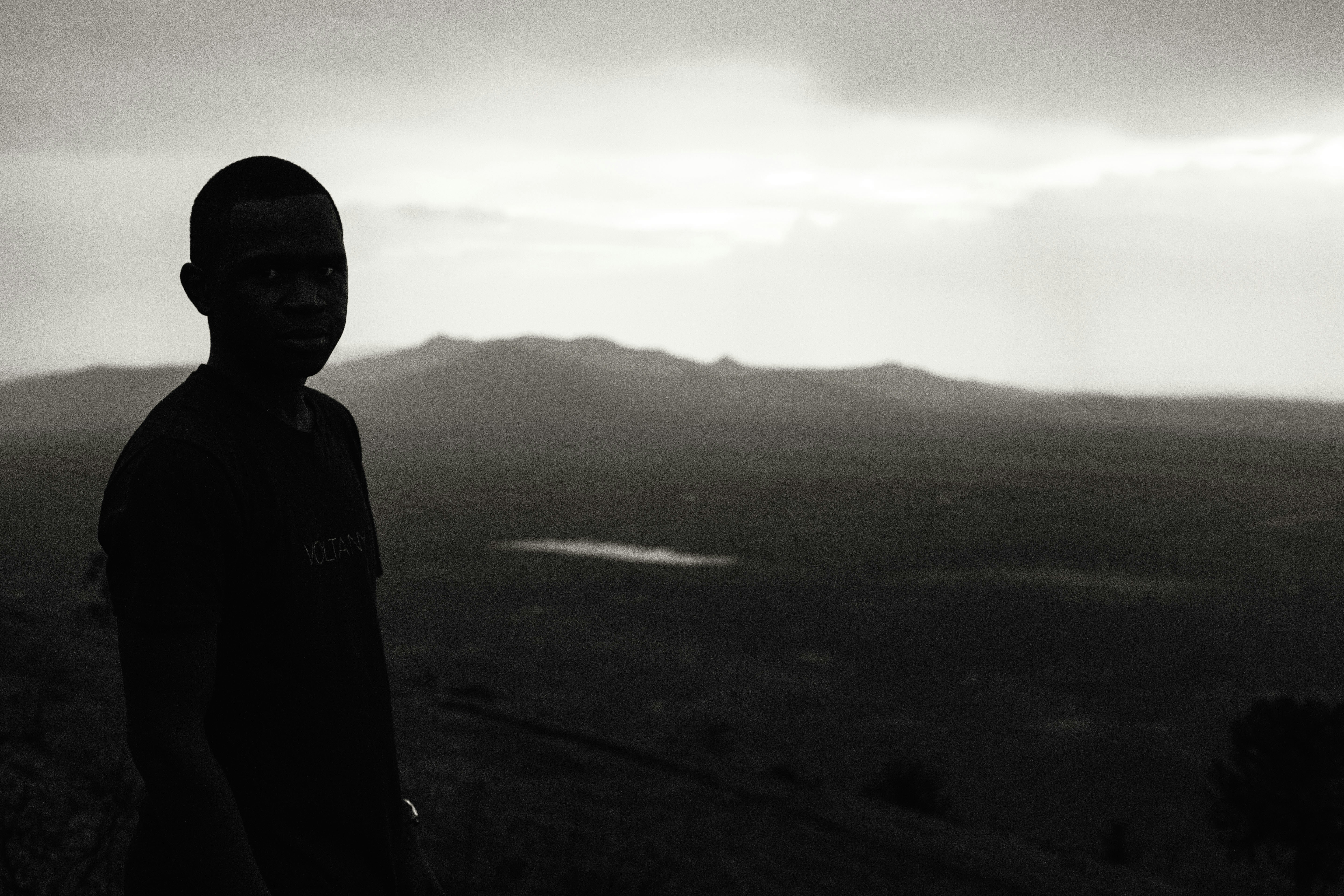 Silhouette of a person with a vast landscape and distant mountains under a cloudy sky.