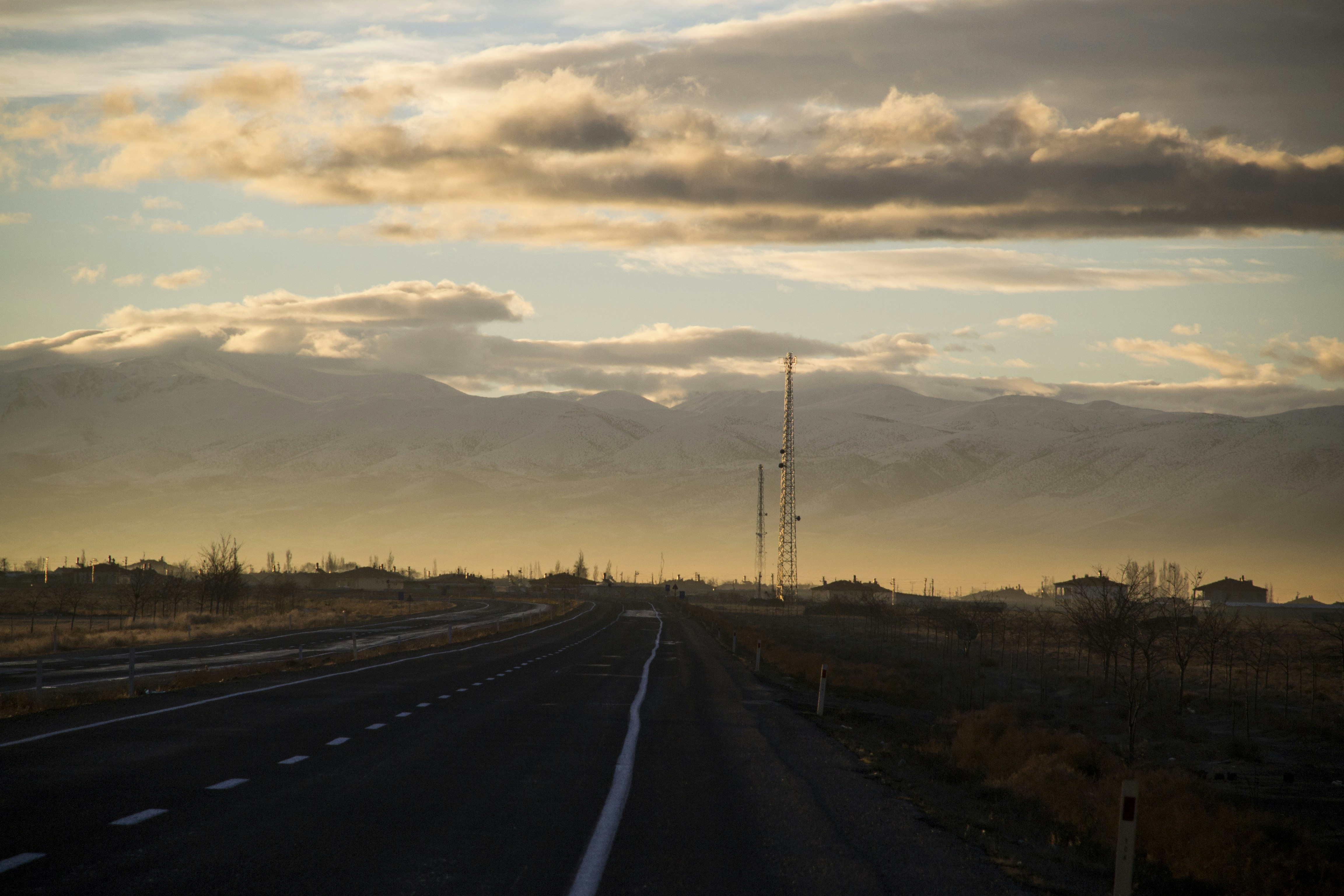 Sunset over a quiet roadway with distant mountains and a dramatic sky.