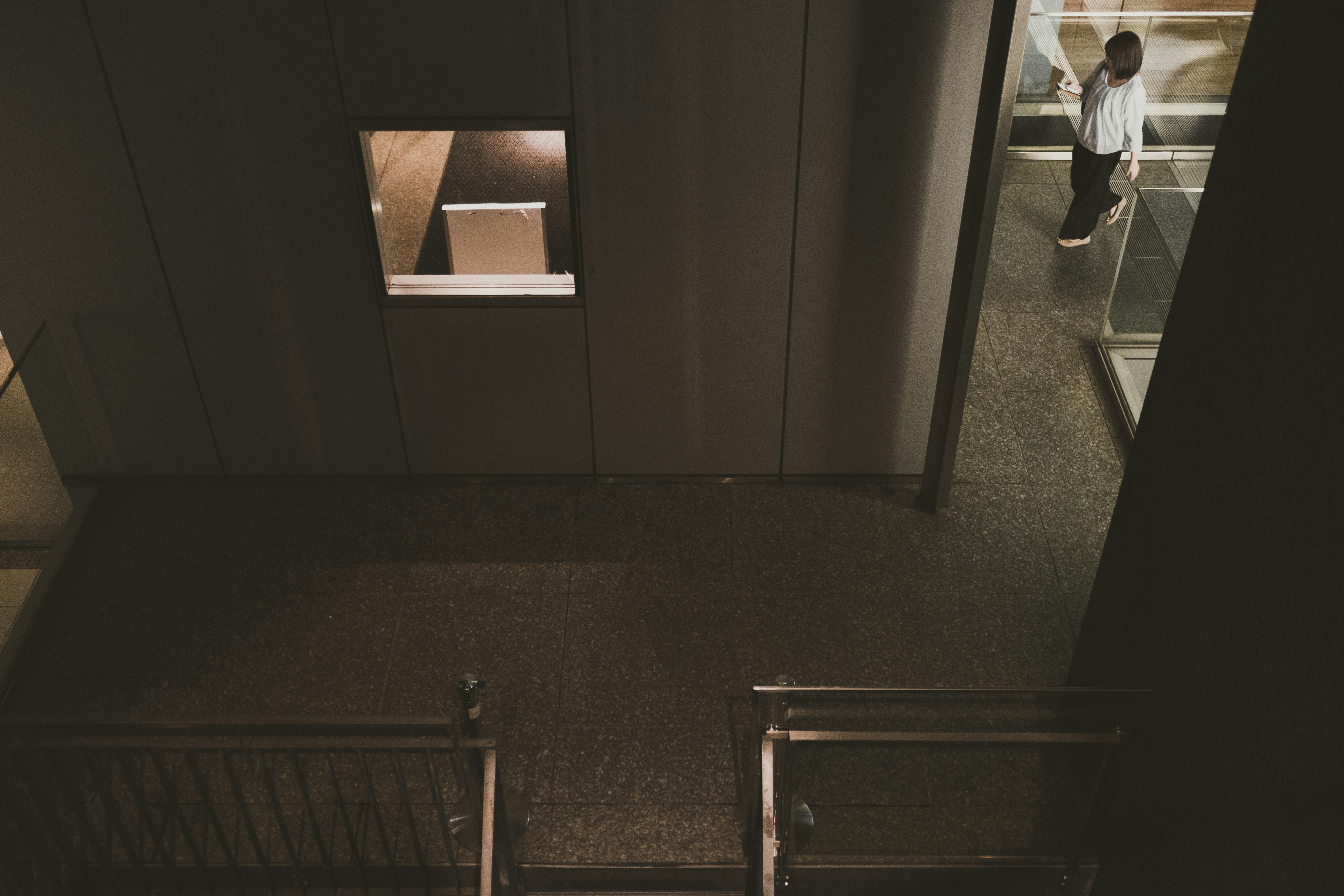 A minimalist interior space featuring a person walking past a window, highlighting the interplay of light and shadow in contemporary design.