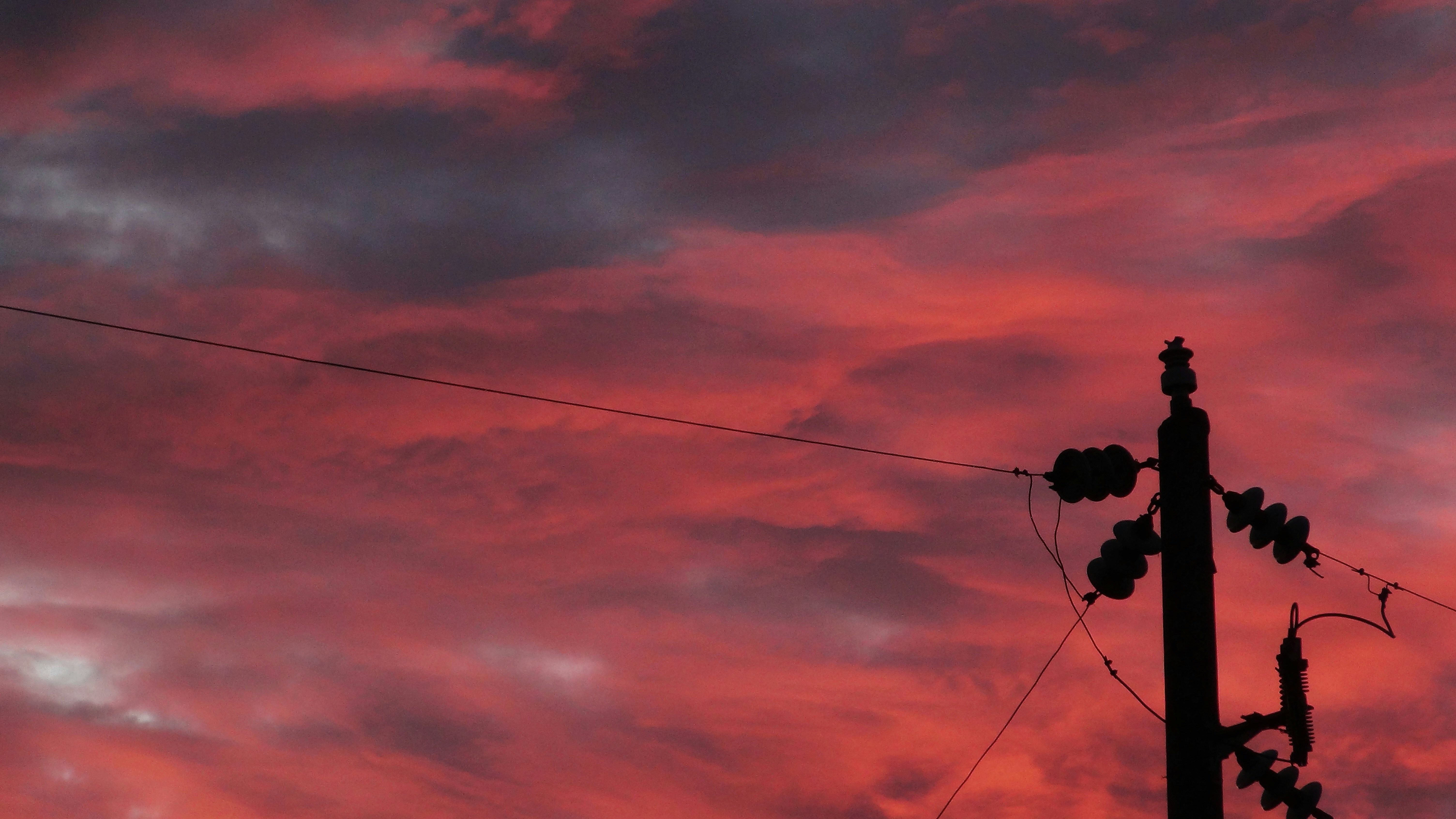 Silhouetted power pole against a vibrant, fiery sky at sunset.