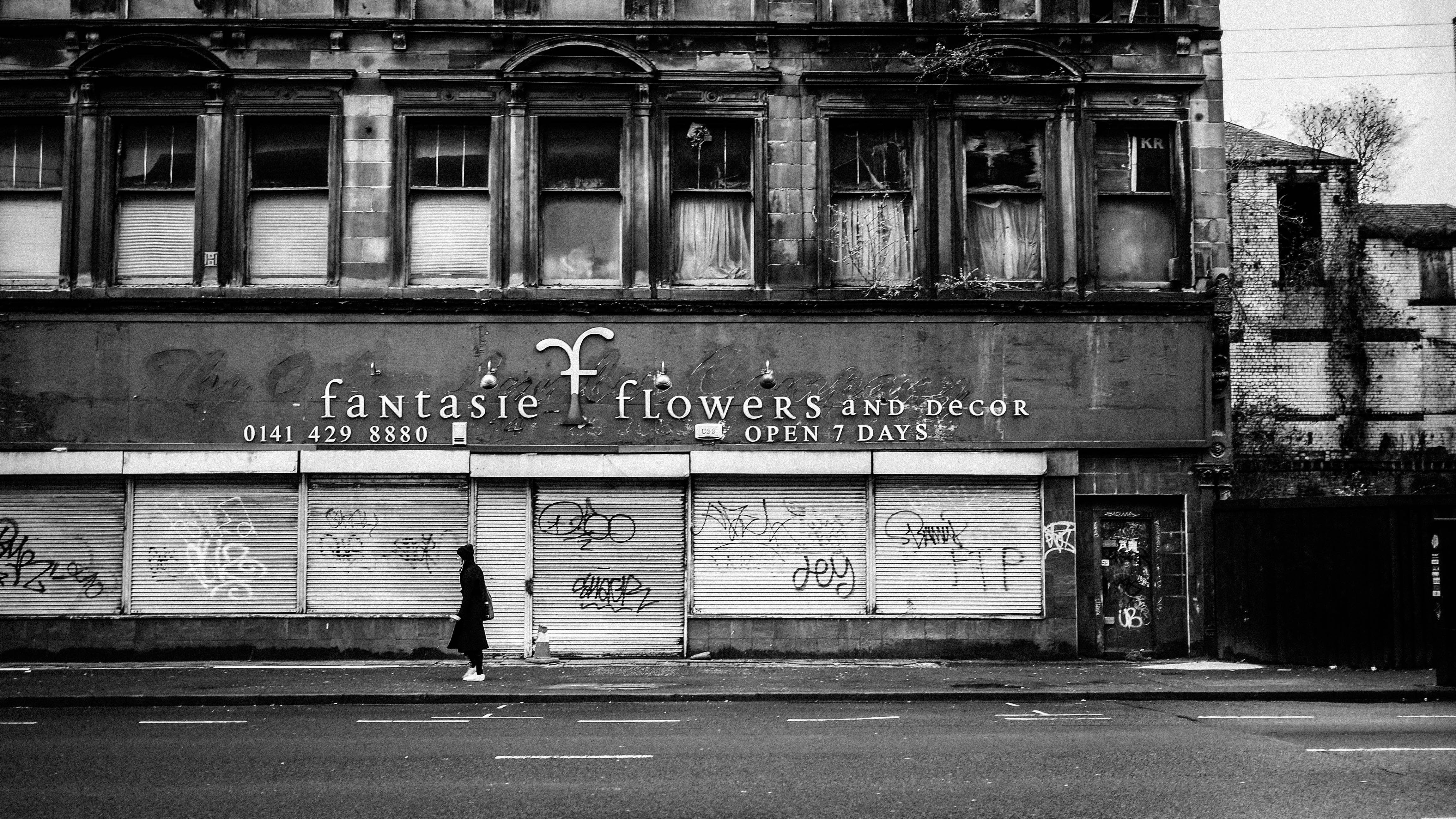 Weathered storefront of Fantasie Flowers adorned with graffiti, showcasing urban decay and resilience. A lone figure walks past, hinting at the passage of time.