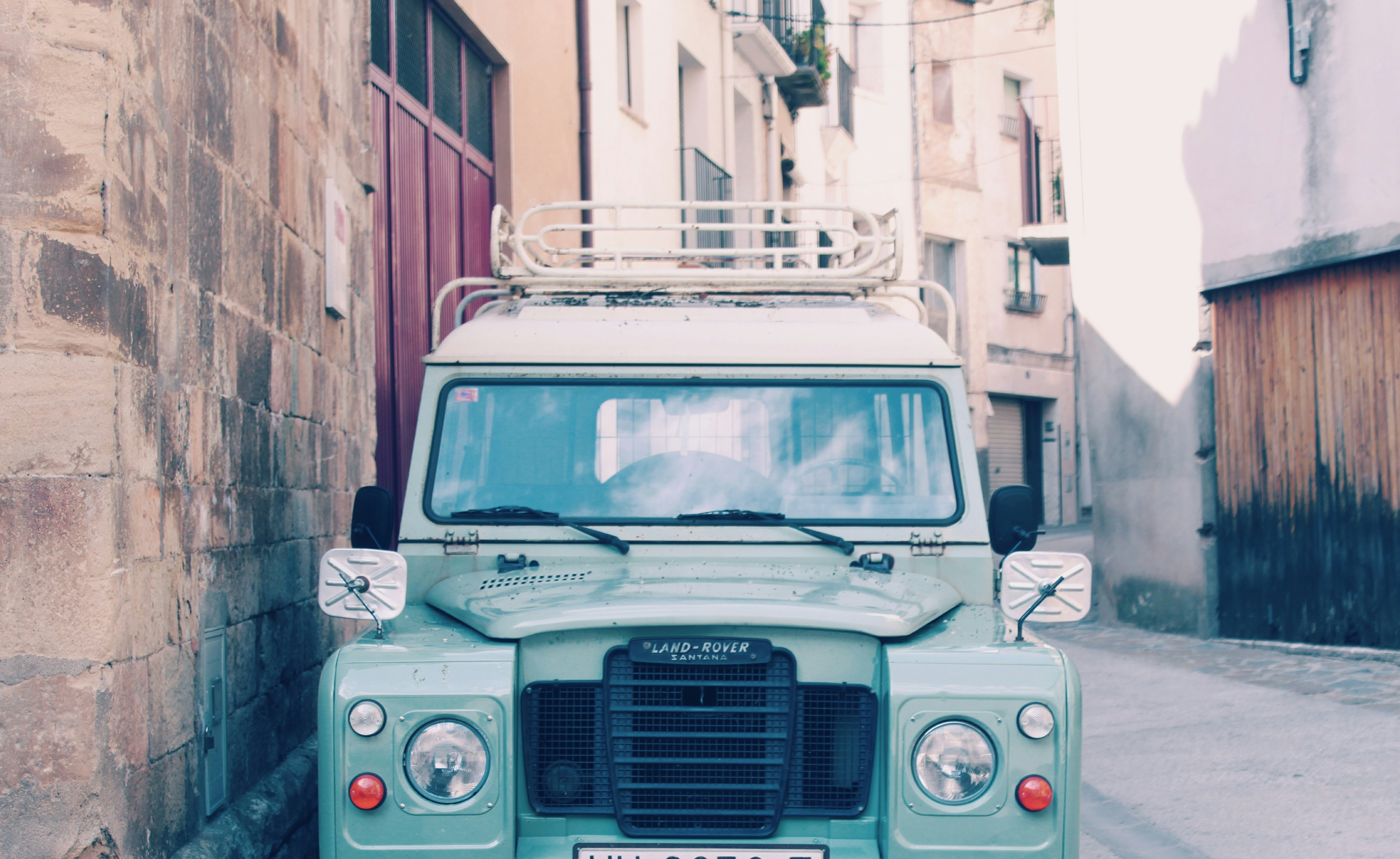 Teal vintage vehicle parked between narrow urban buildings.