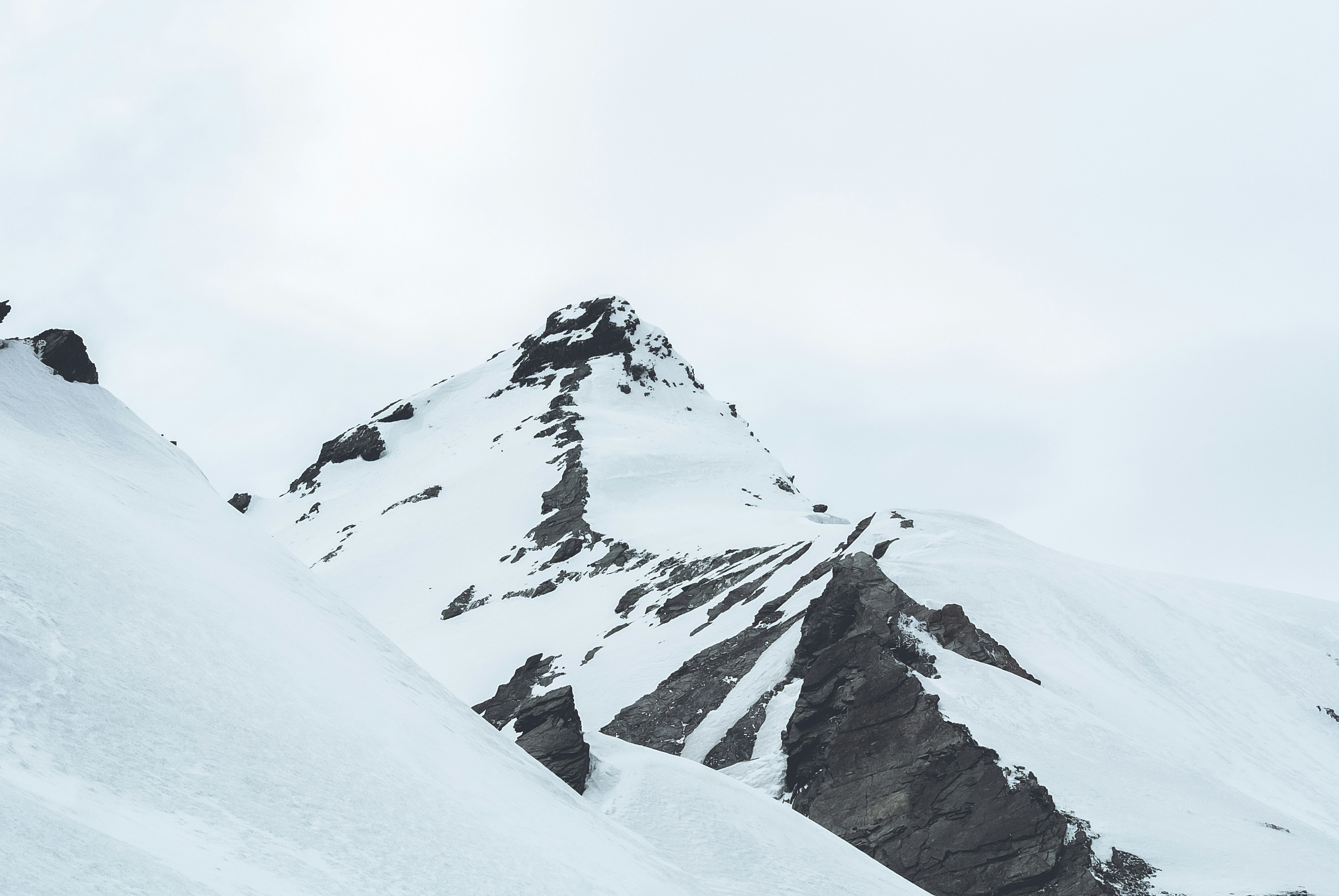 Jagged snow-covered peak rises against a soft gray sky, showcasing the stark beauty of winter landscapes.