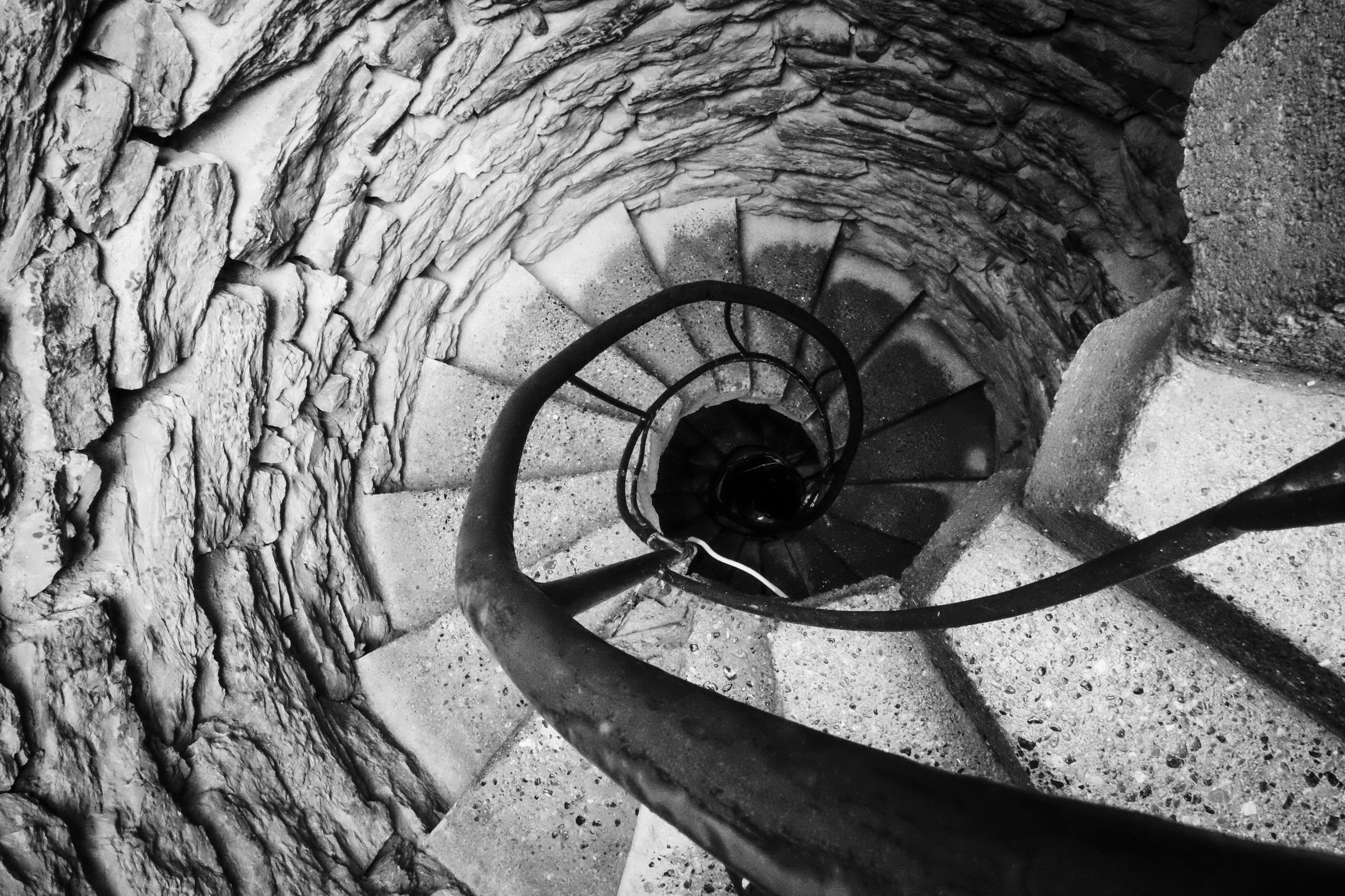 Black and white spiral staircase with textured stone walls.