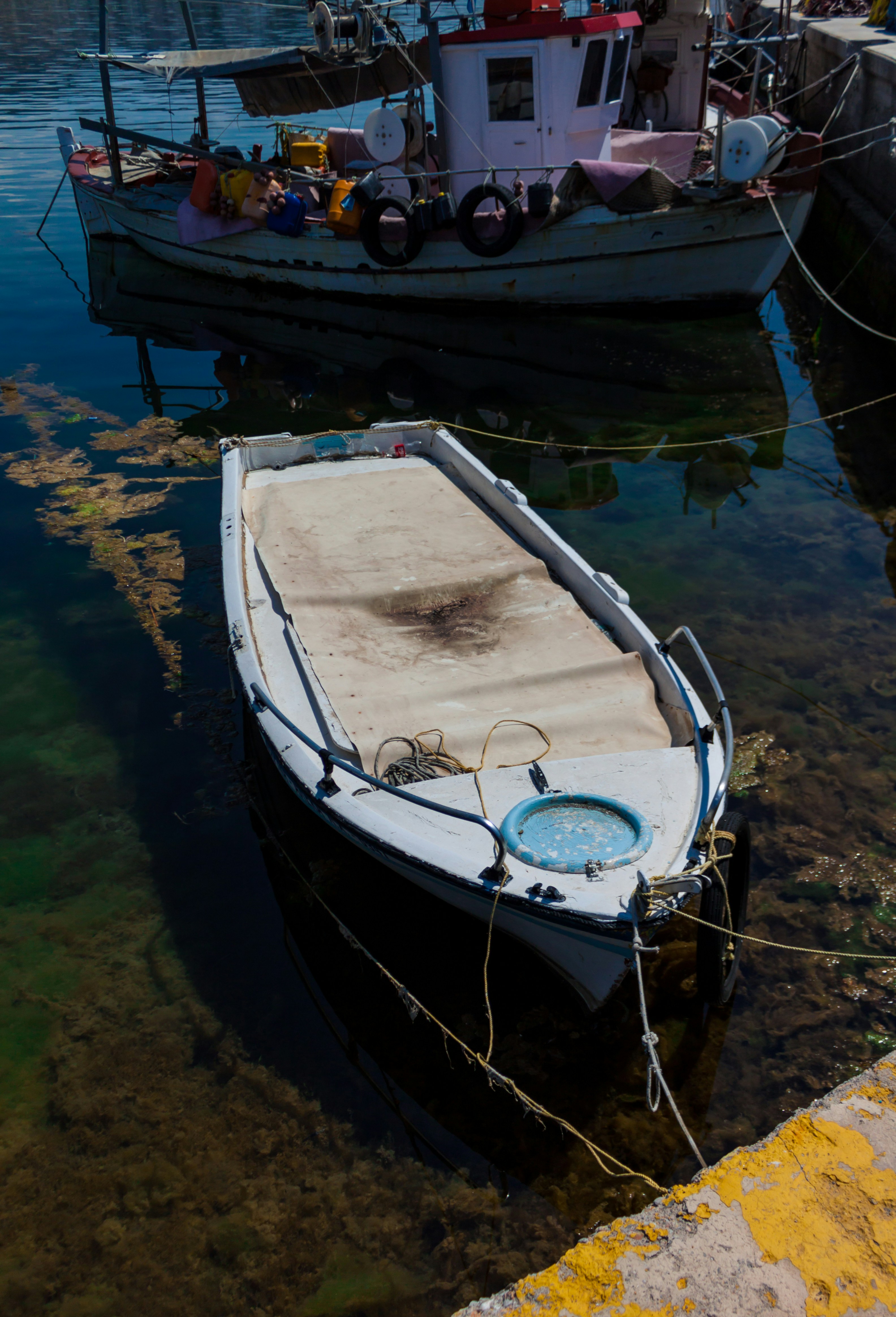 Small fishing boat anchored in tranquil waters, surrounded by reflections and a larger vessel in the background.