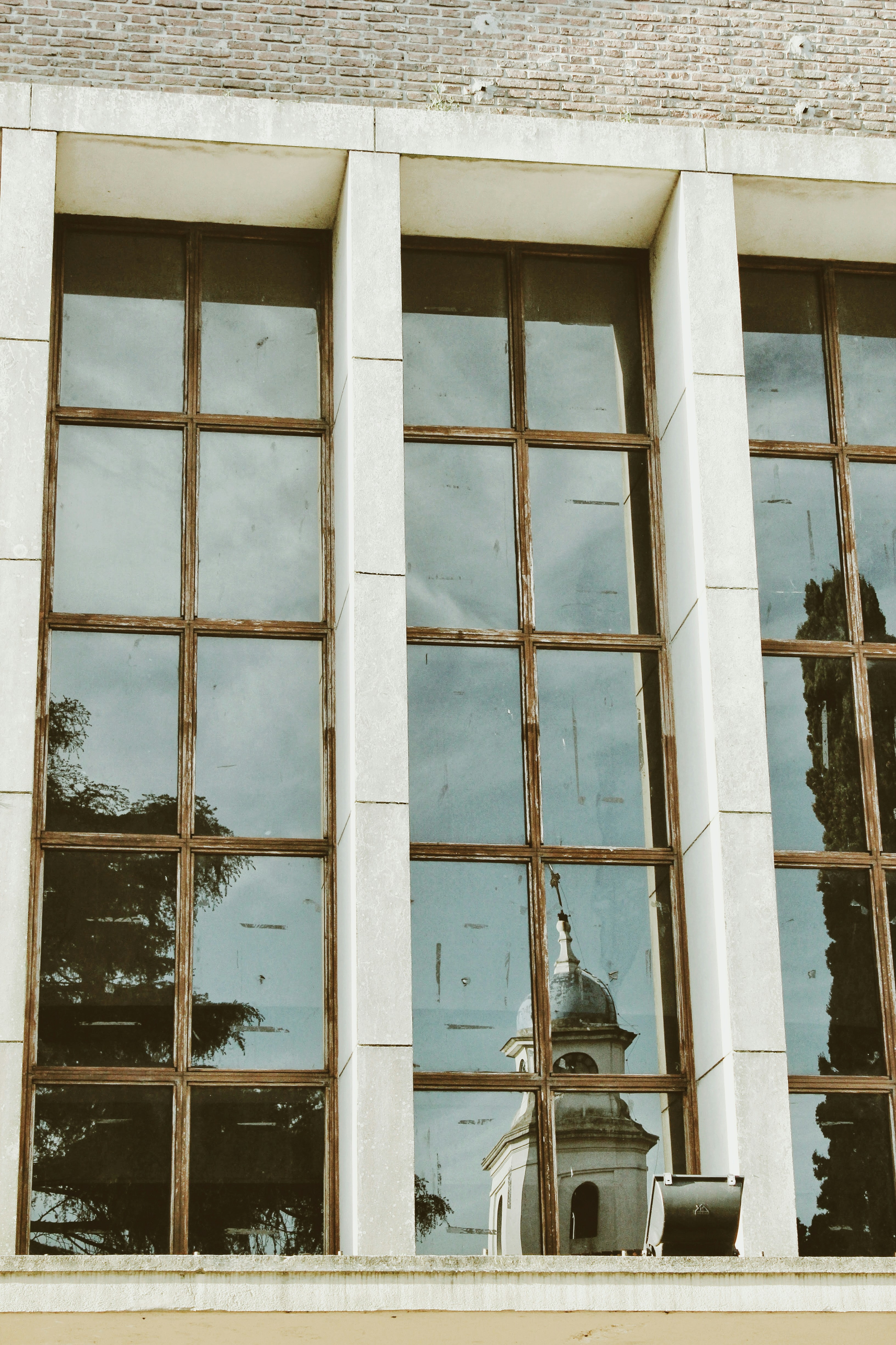 Reflections of a church steeple in large, grid-patterned windows of a modern building, juxtaposing old and new architecture.