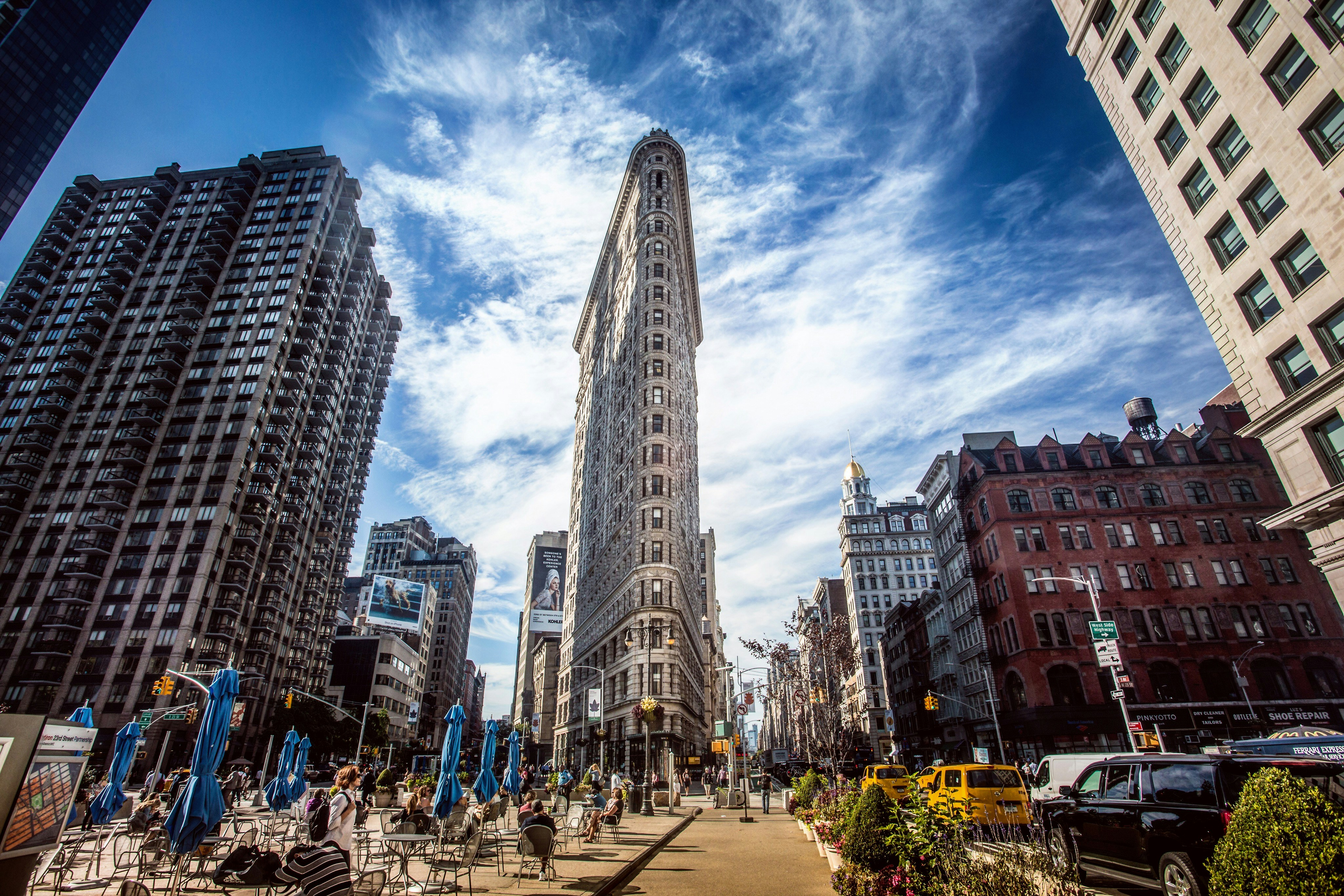 Flatiron Building rising against a backdrop of dynamic clouds and bustling city life.