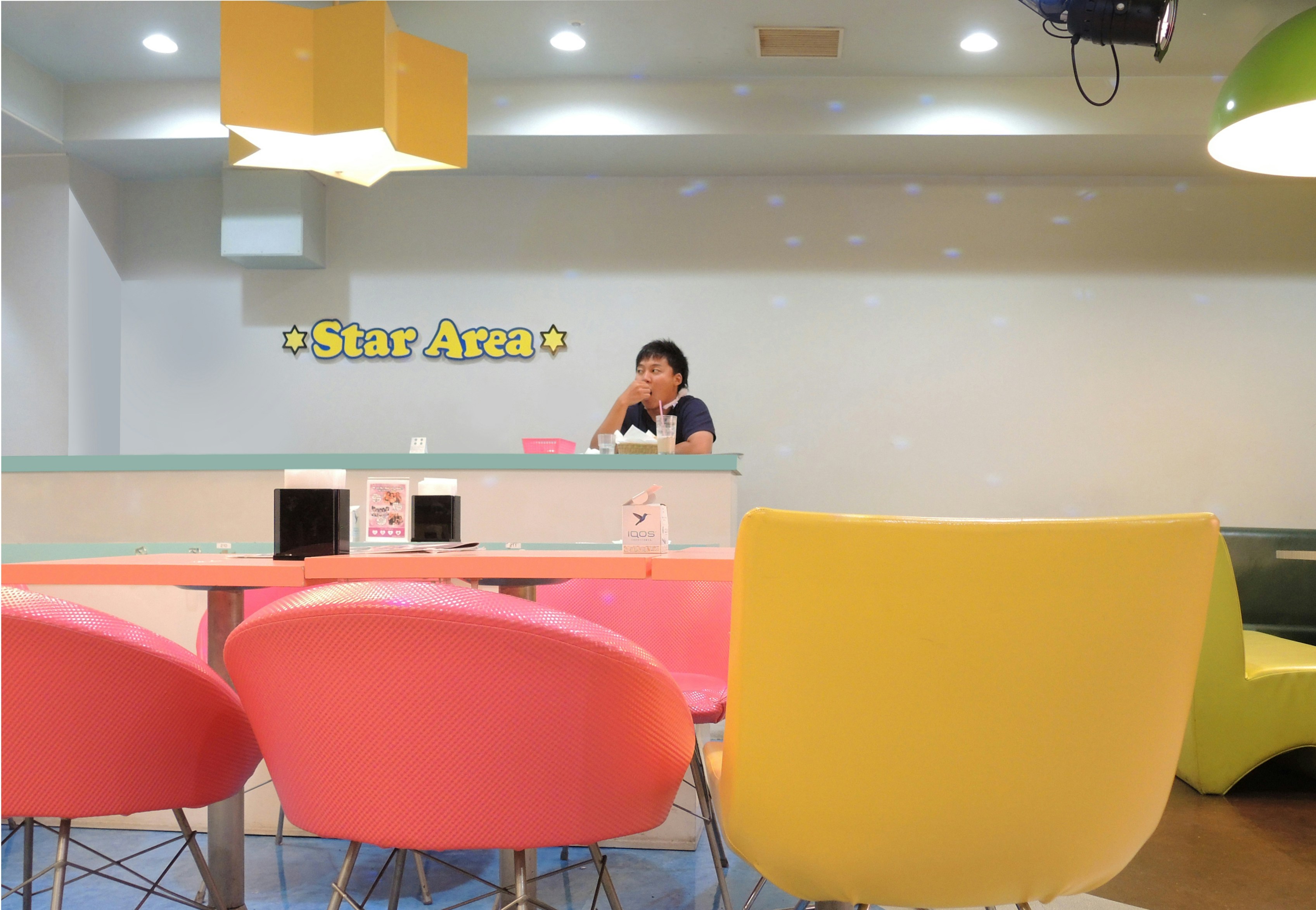 Cafe interior with pastel pink and yellow chairs and a counter where a person sits beneath a Star Area sign.