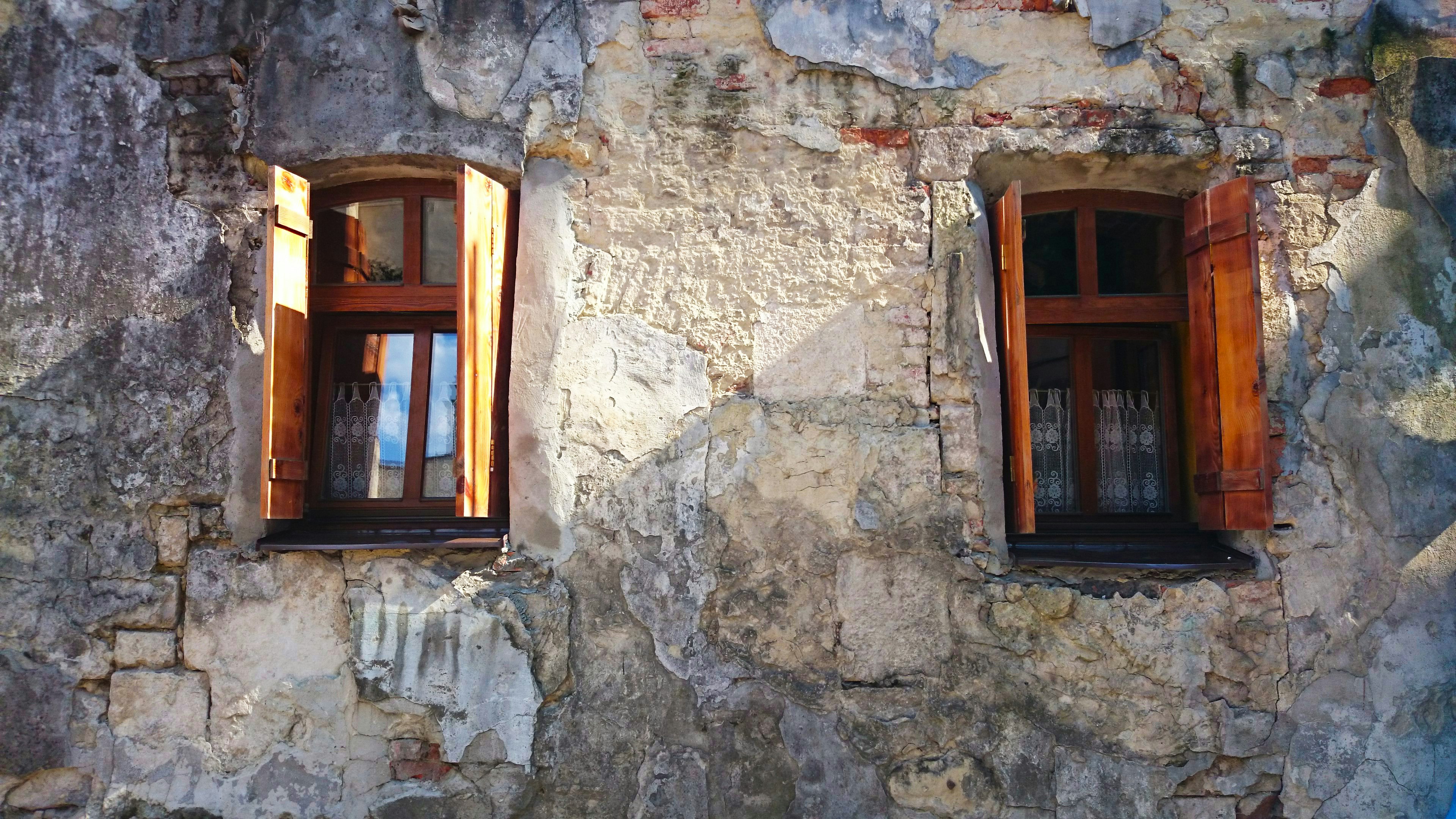 Two wooden windows with open shutters reveal a glimpse of history against a weathered stone wall. The texture and colors tell a story of age and resilience.