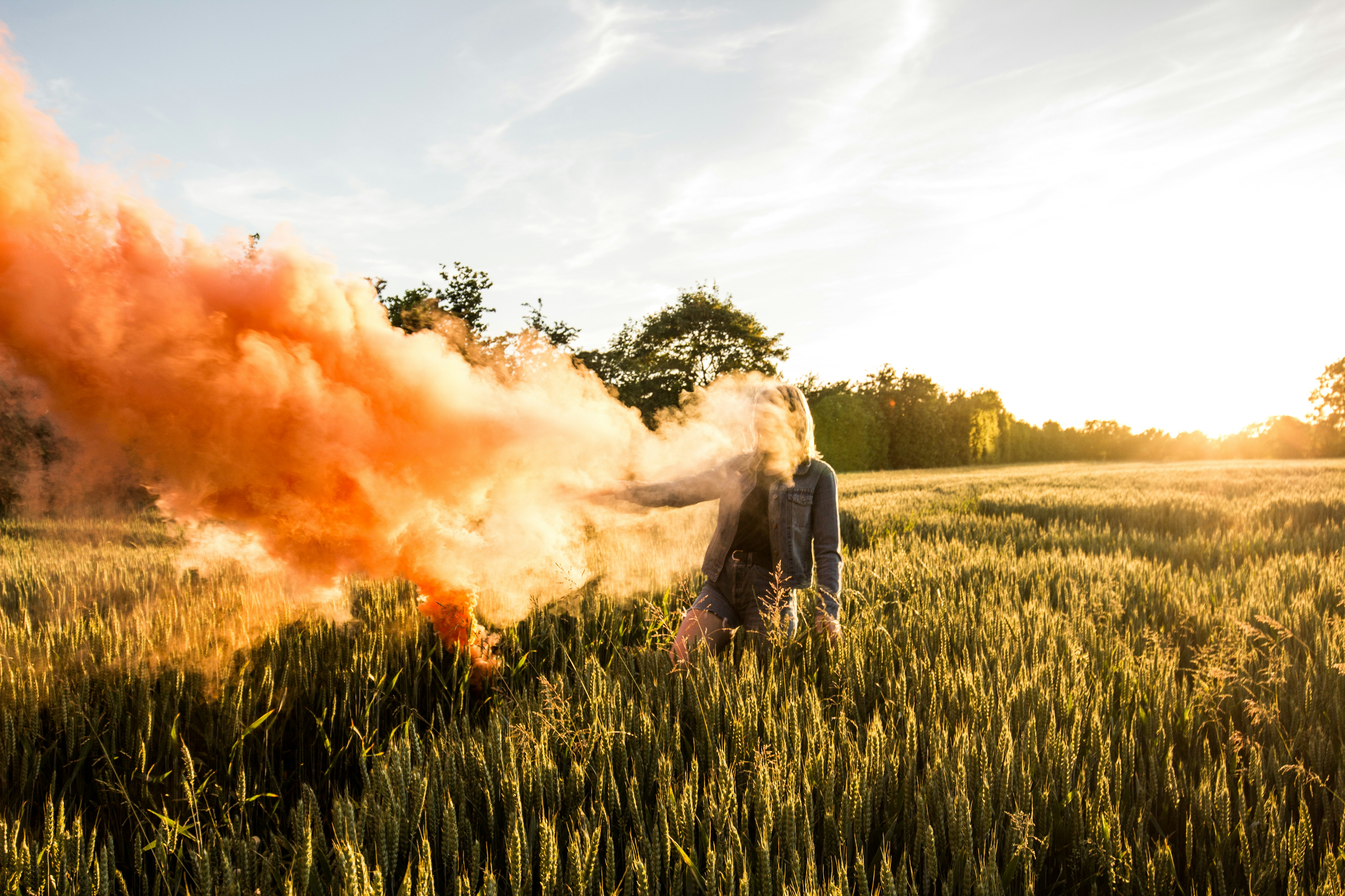 Two figures enveloped in vibrant orange smoke amidst a golden wheat field during sunset.