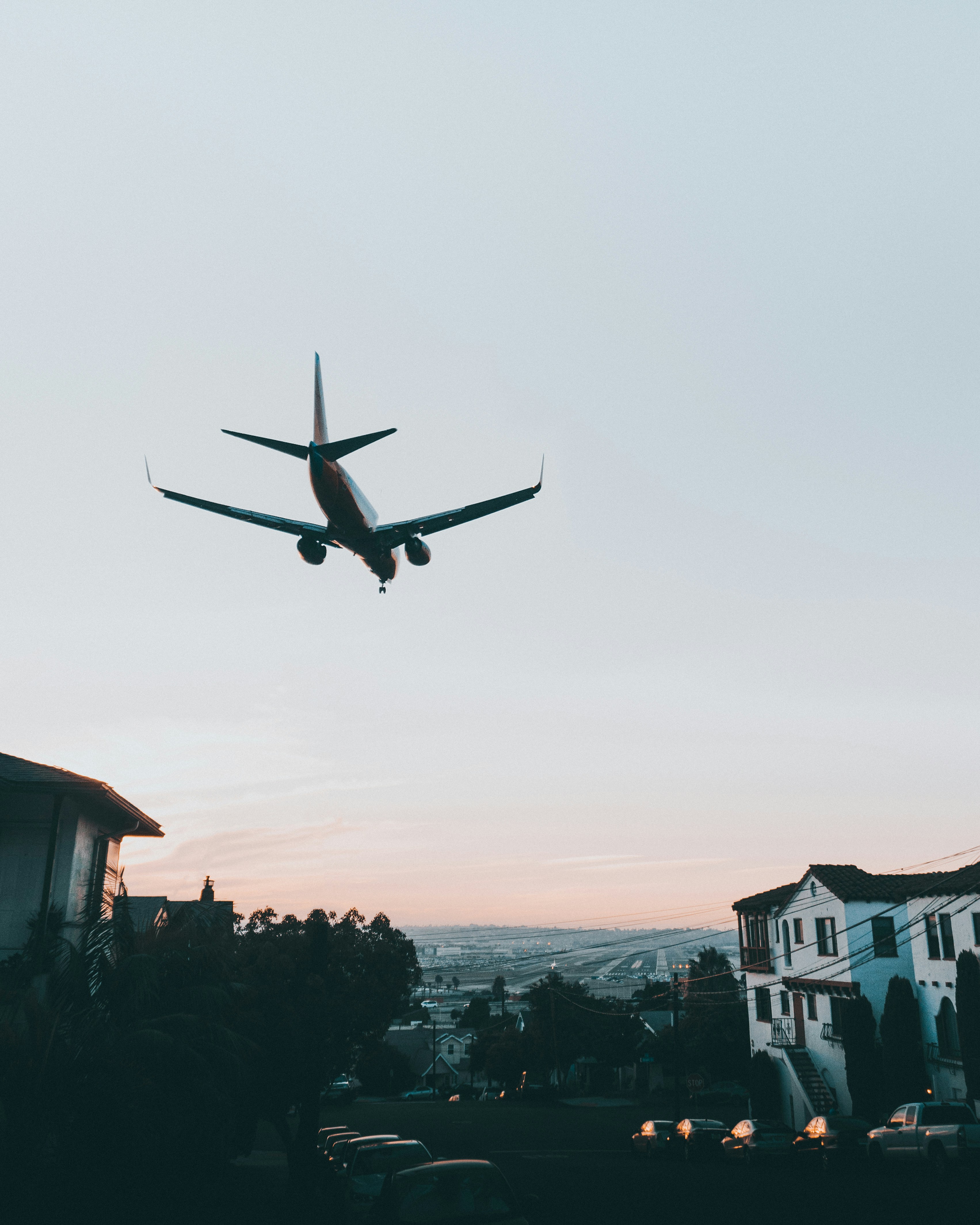 Commercial airplane approaching landing over a residential neighborhood at dusk, with a gradient sky in the background.