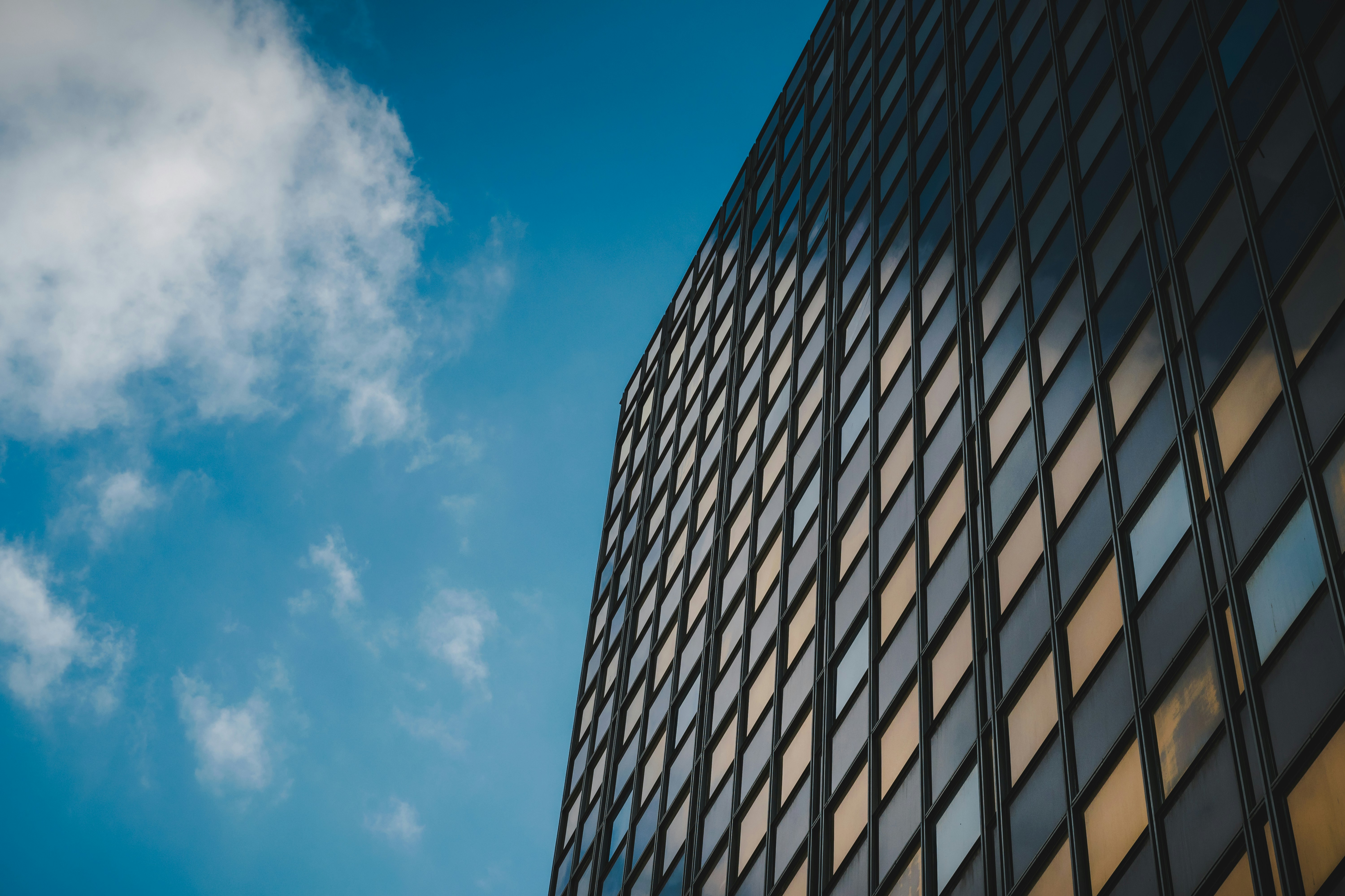 Modern high-rise with reflective windows against a vivid blue sky and scattered clouds.
