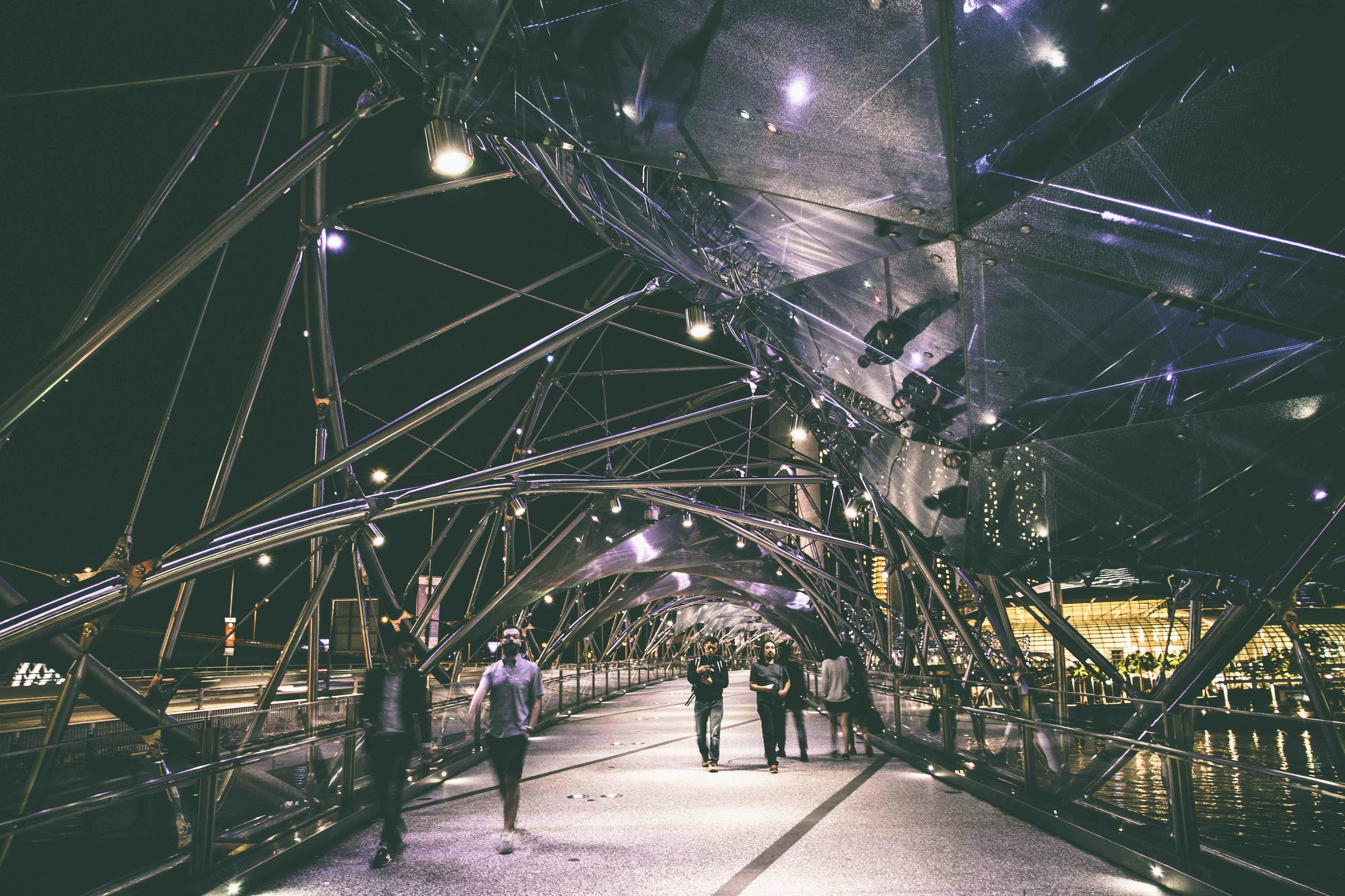 People walking under a geometric steel structure at night, illuminated by soft artificial lights.