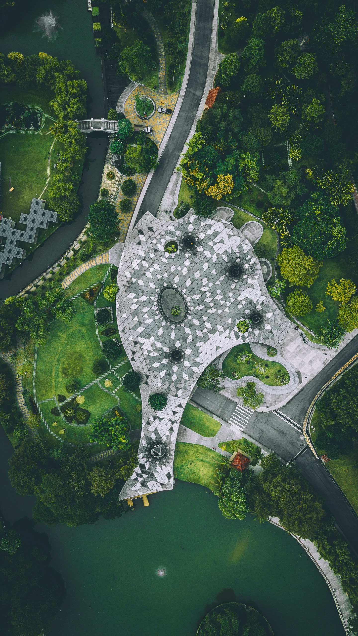 Aerial view of a uniquely designed pavilion surrounded by lush greenery and winding pathways, showcasing a harmonious blend of nature and modern design.