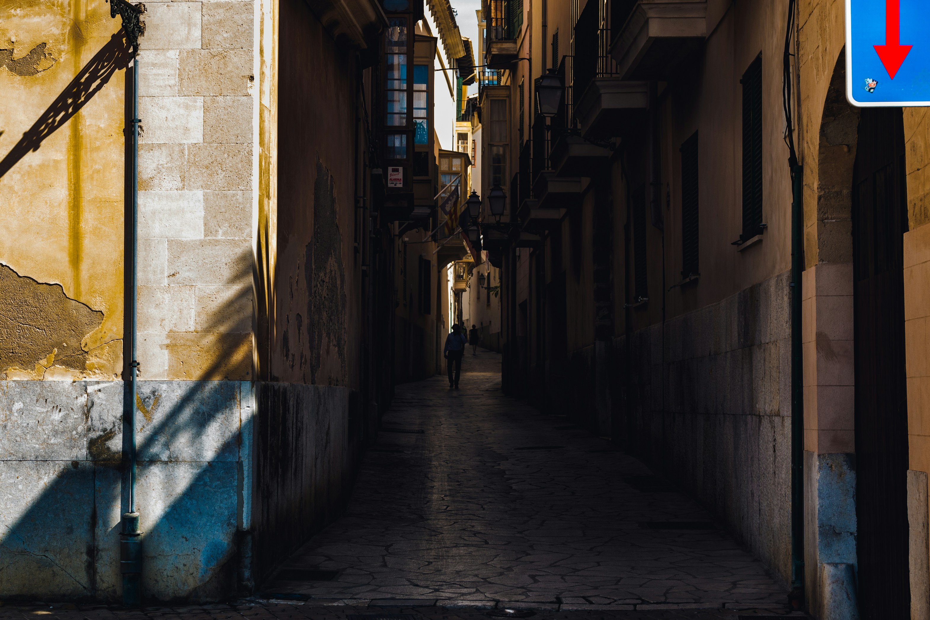 Narrow alleyway with deep shadows and a lone figure walking towards the light.