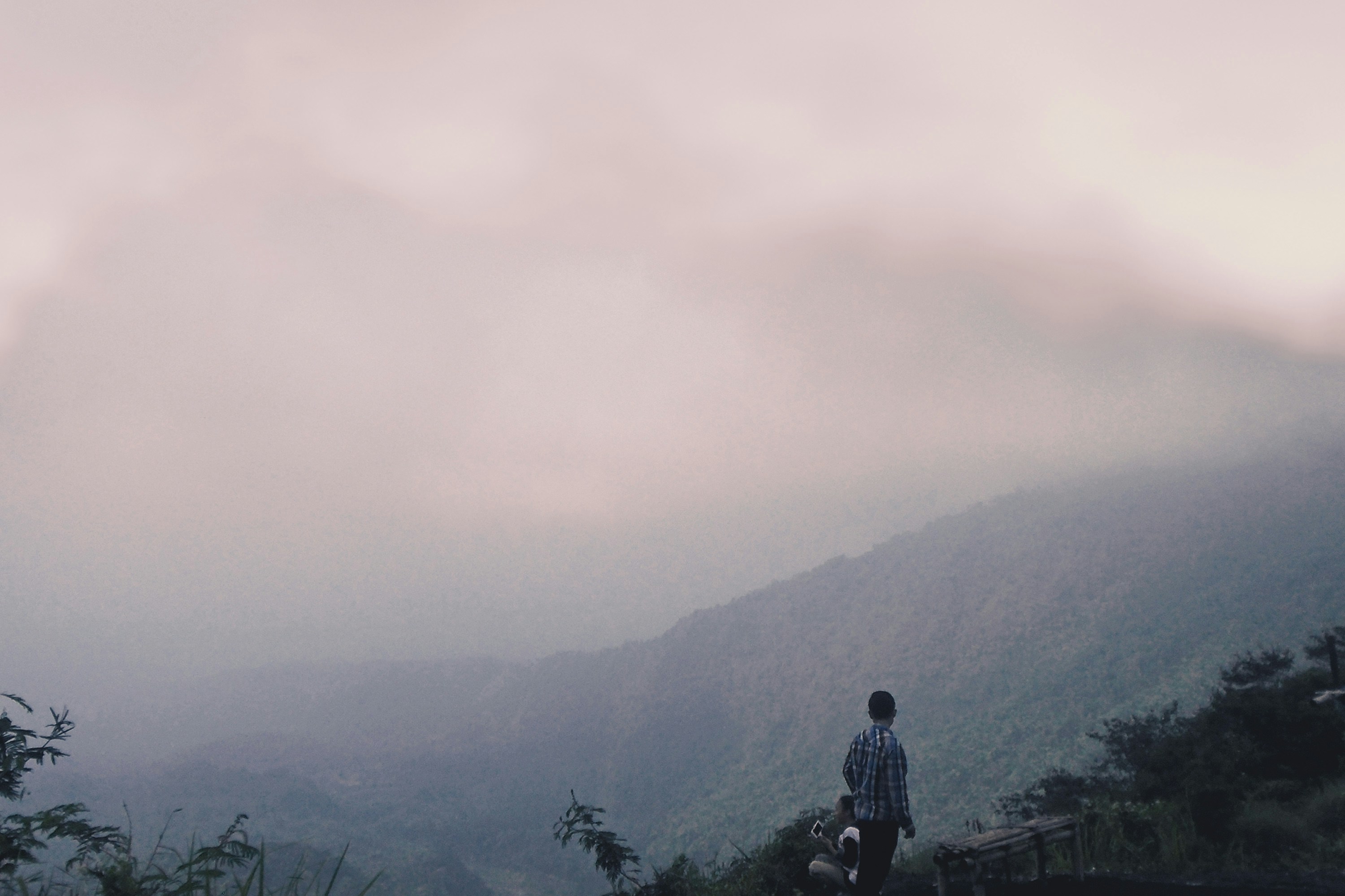 Person standing on a hillside overlooking a fog-covered valley at dawn.