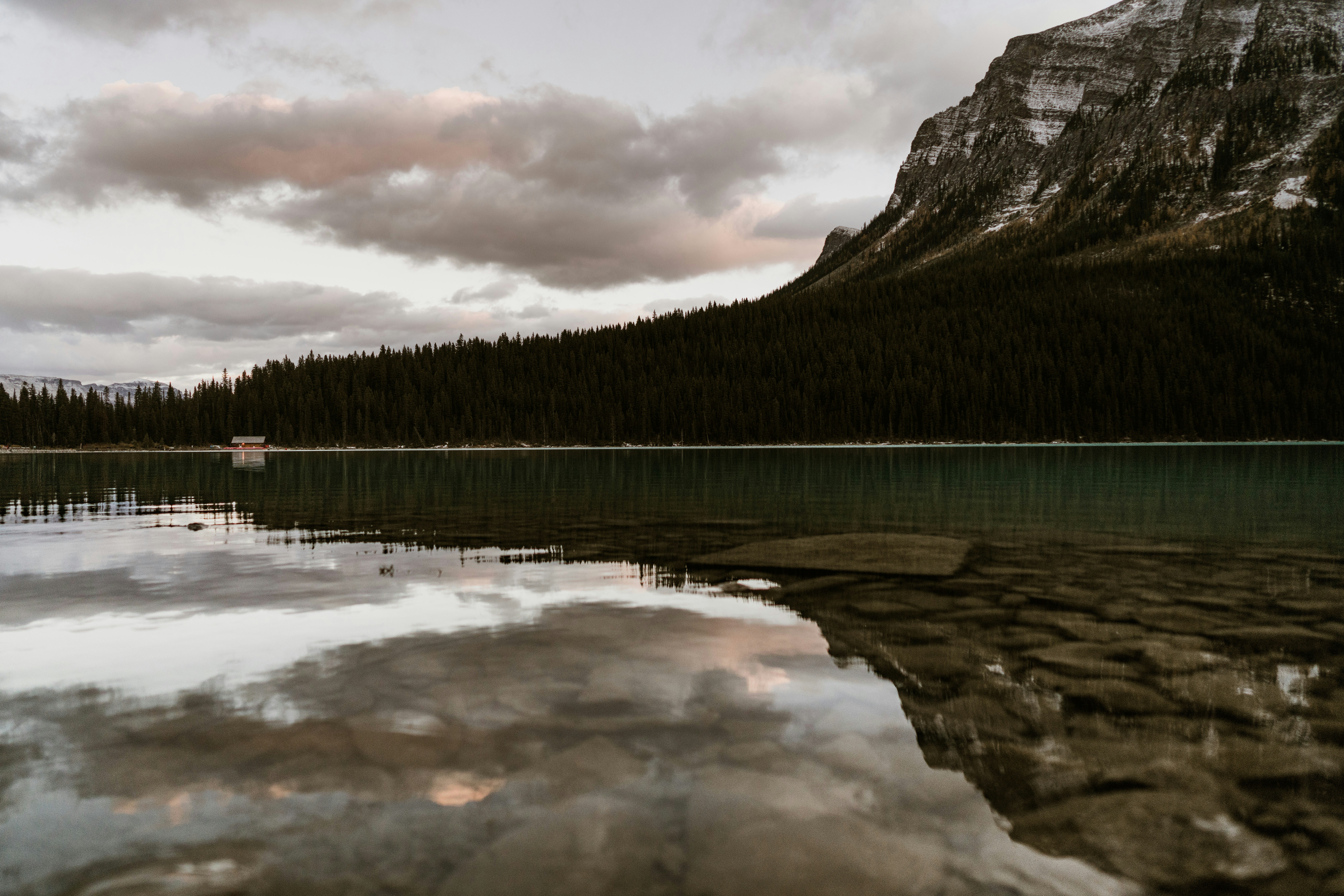 Calm lake reflecting a cloudy sky beneath a towering mountain.