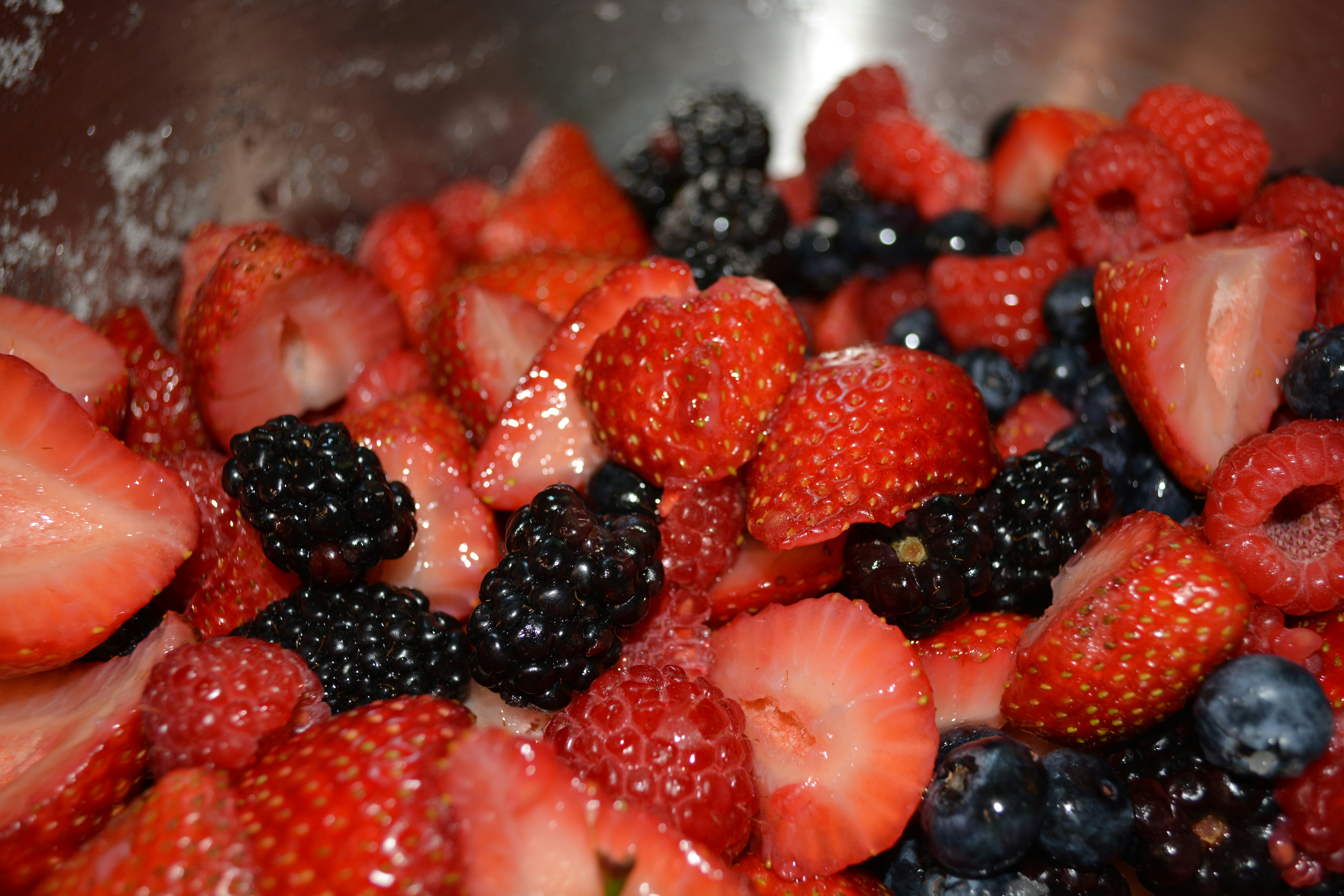 Assorted fresh berries including sliced strawberries, blackberries, raspberries, and blueberries in a metal bowl.