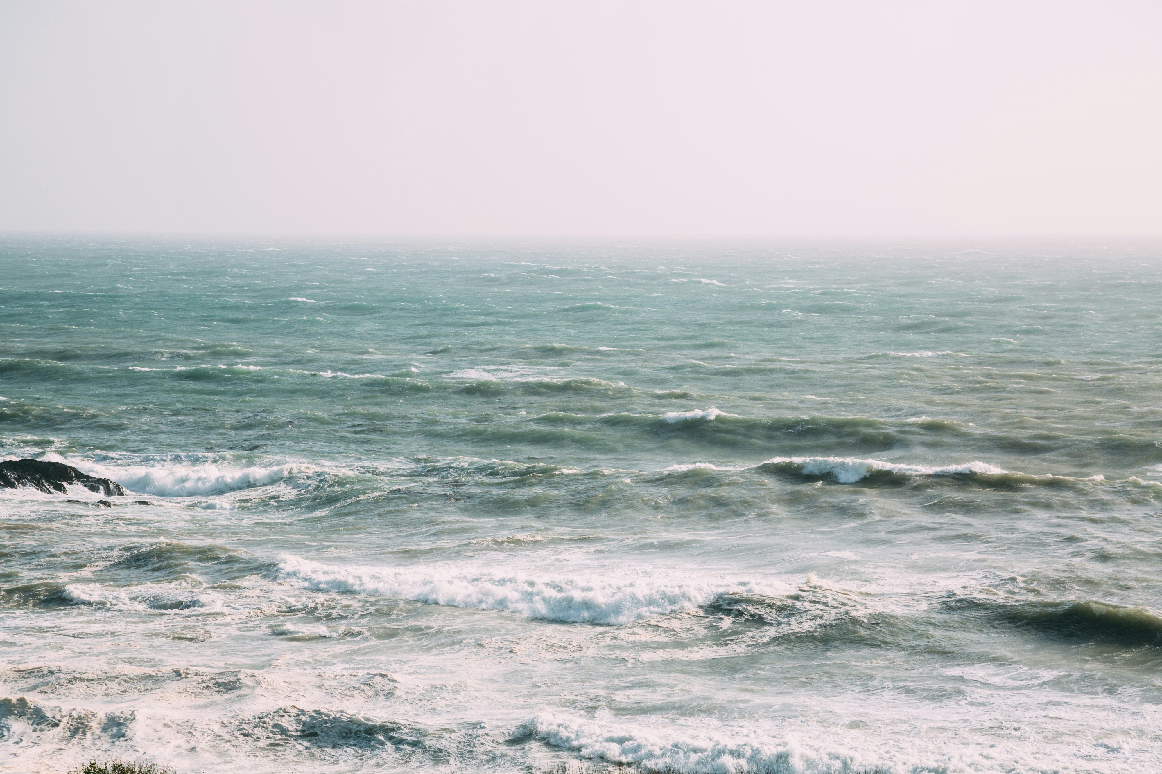 Waves crash against rocky shores under a misty sky, evoking a sense of solitude and the power of nature.